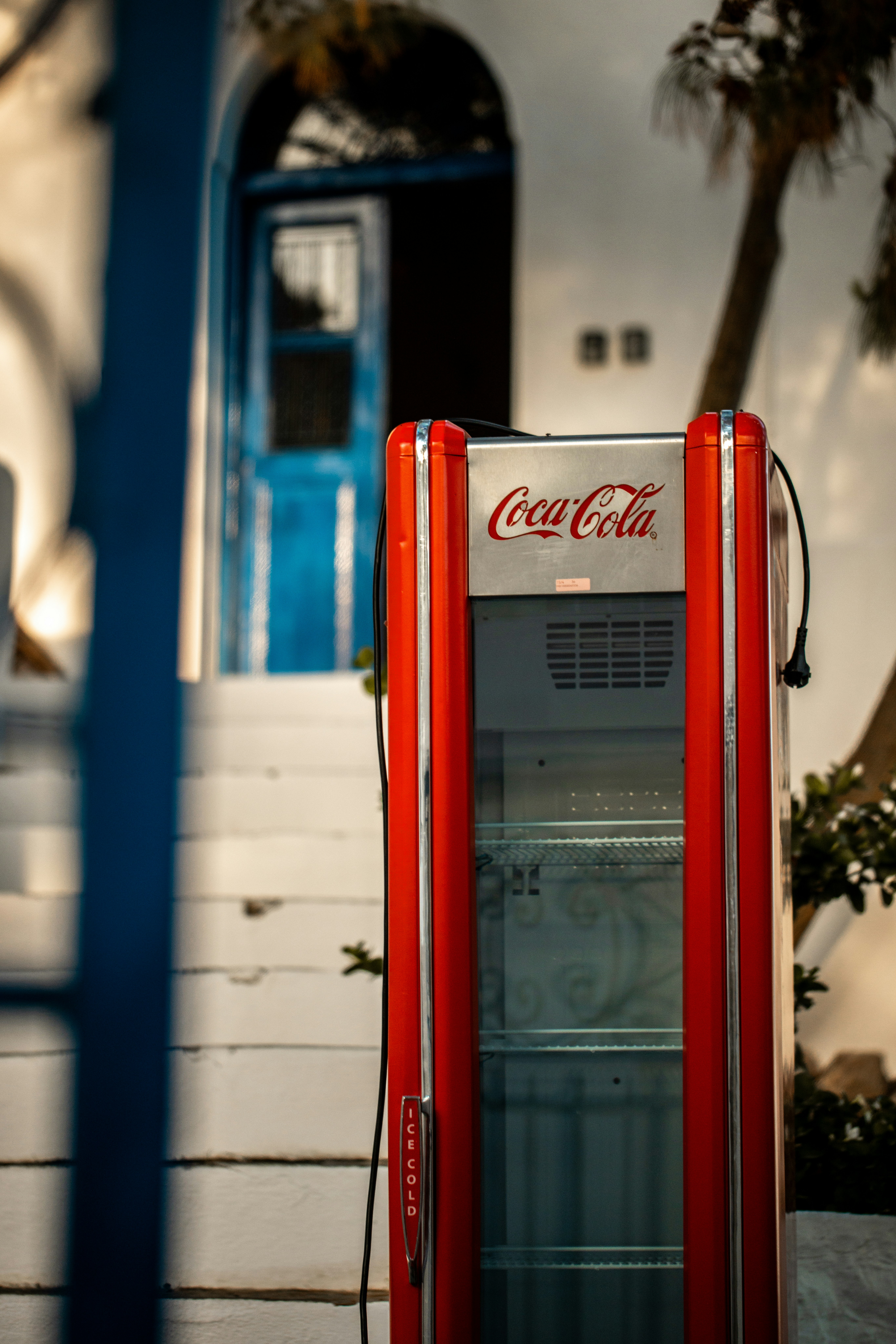 Red coca-cola refrigerator by a blue door in greece