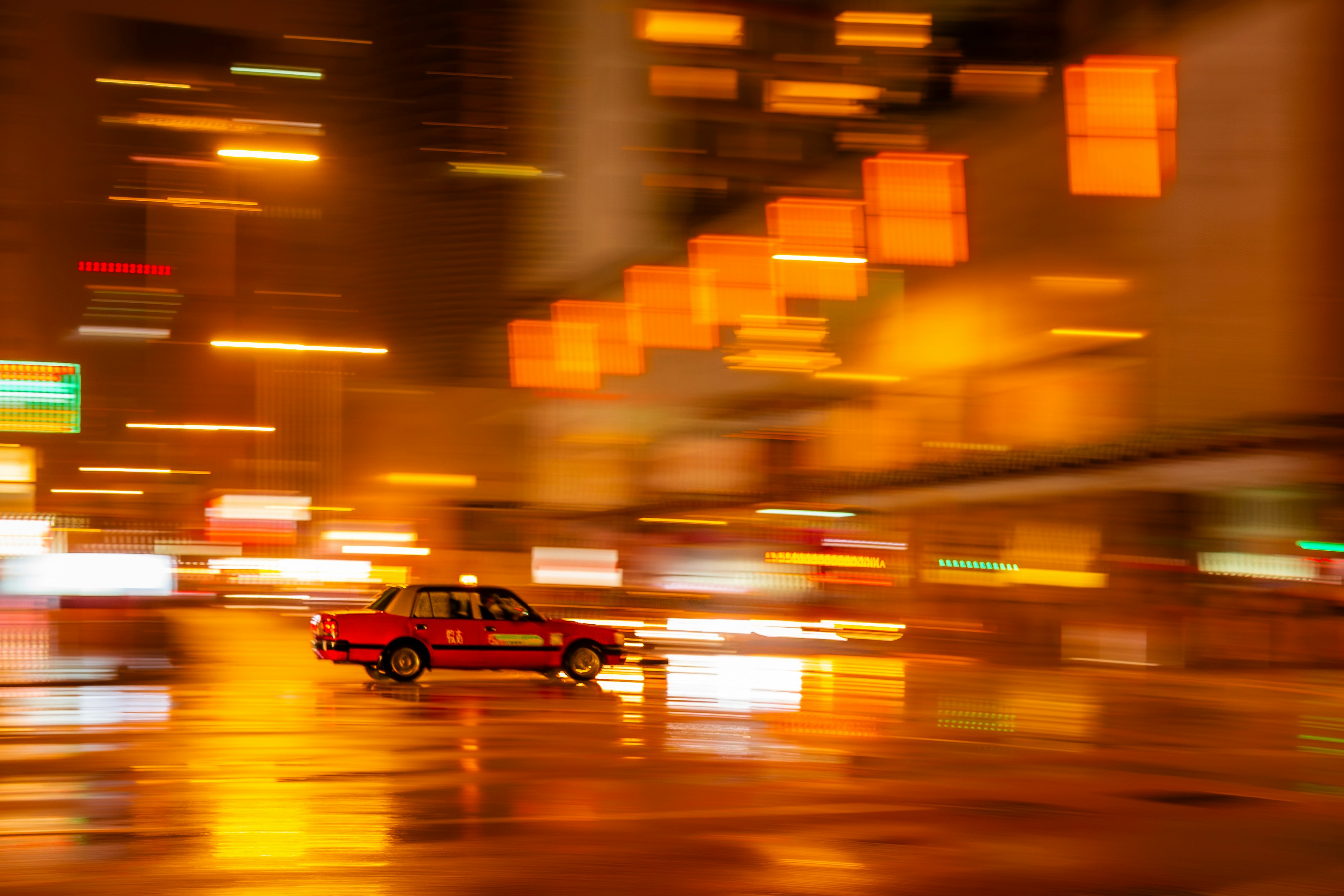 A red taxi speeds through a blurry, light-filled city night.