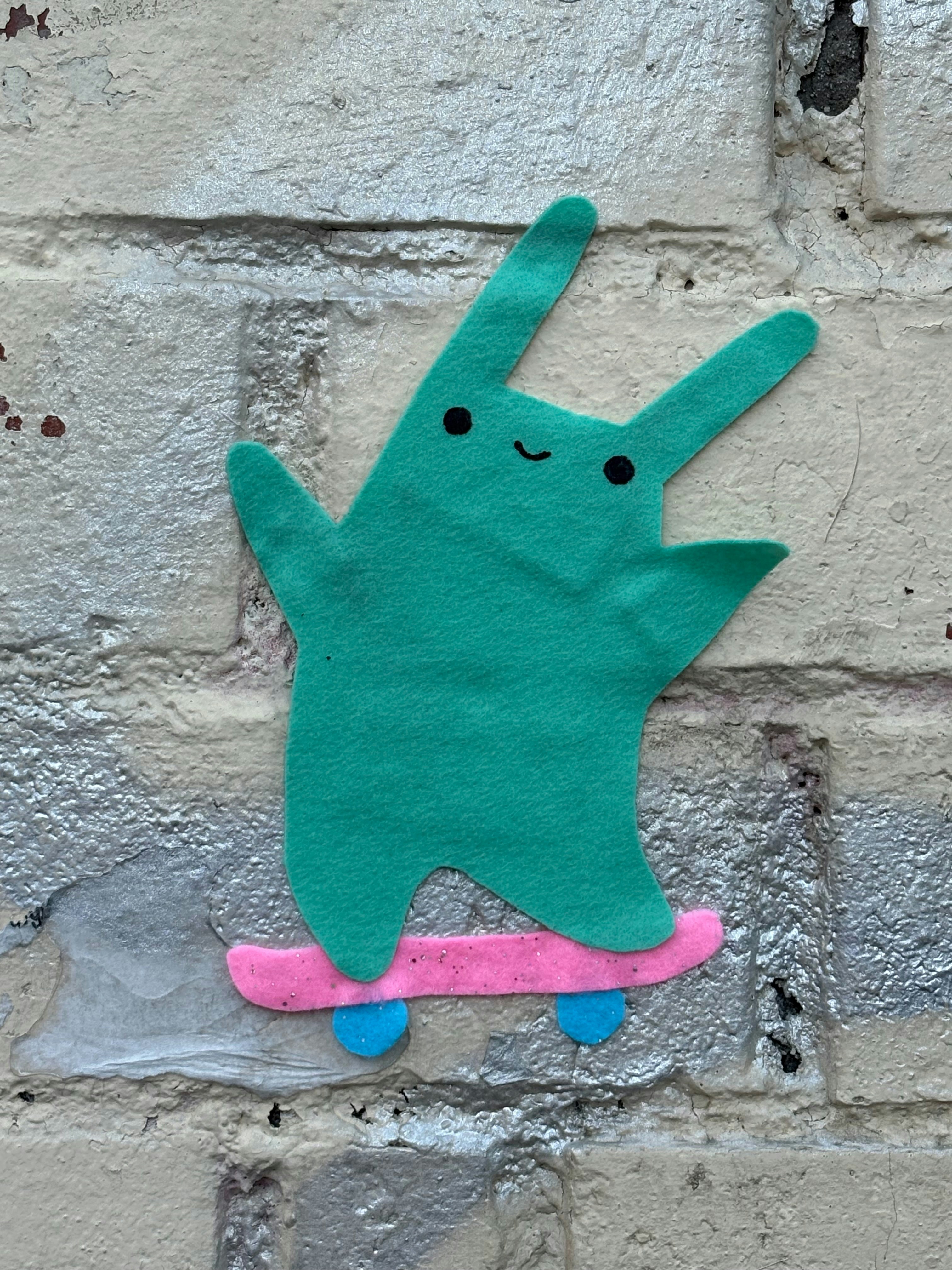 Teal skate-away: graffiti character stuck on a sunlit brick wall