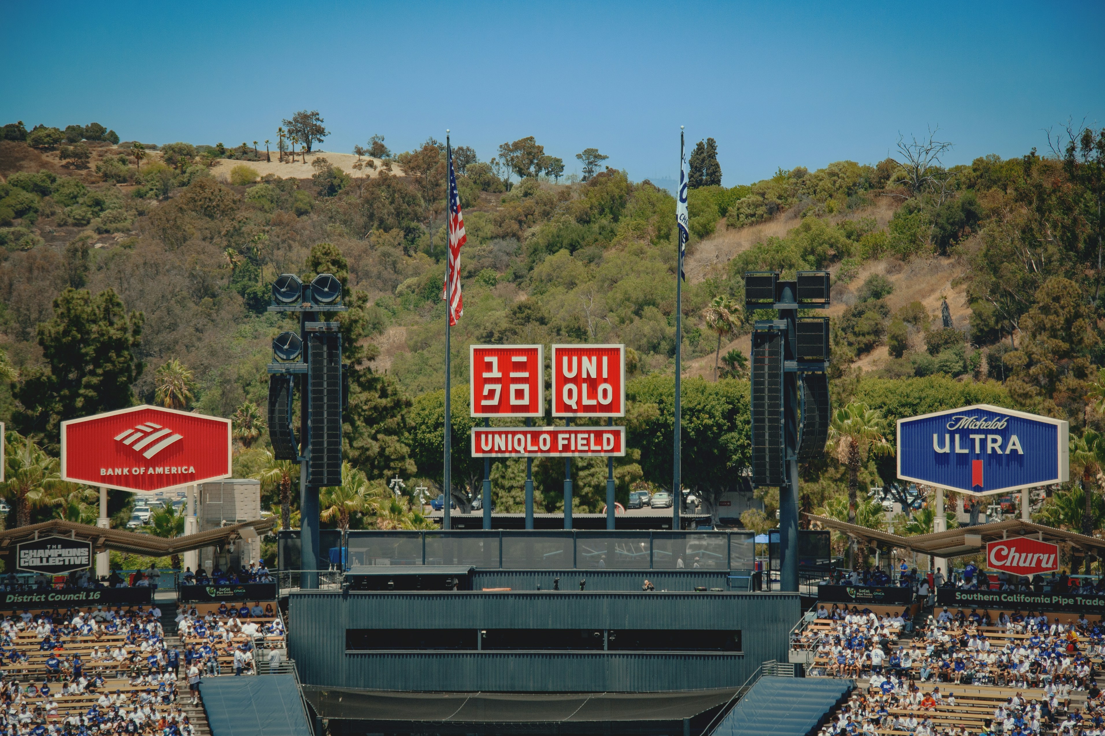 Wide stadium view with prominent UNIQLO Field sign and banners; crowd seating visible, flagpoles and stage-like structure centered in frame.