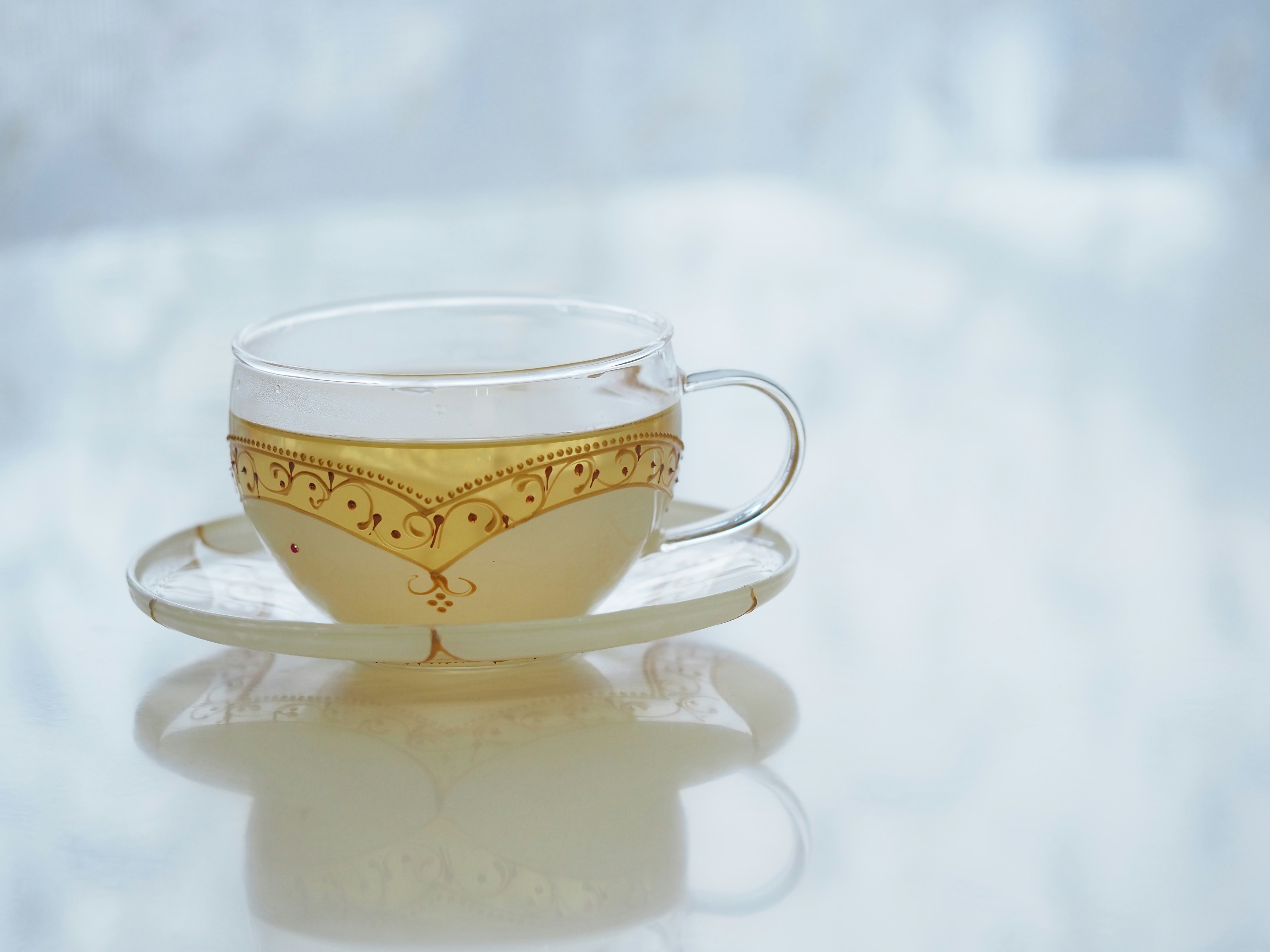 Delicate Tea Moment: A Glass Cup Reposing on a Saucer with Soft Reflections