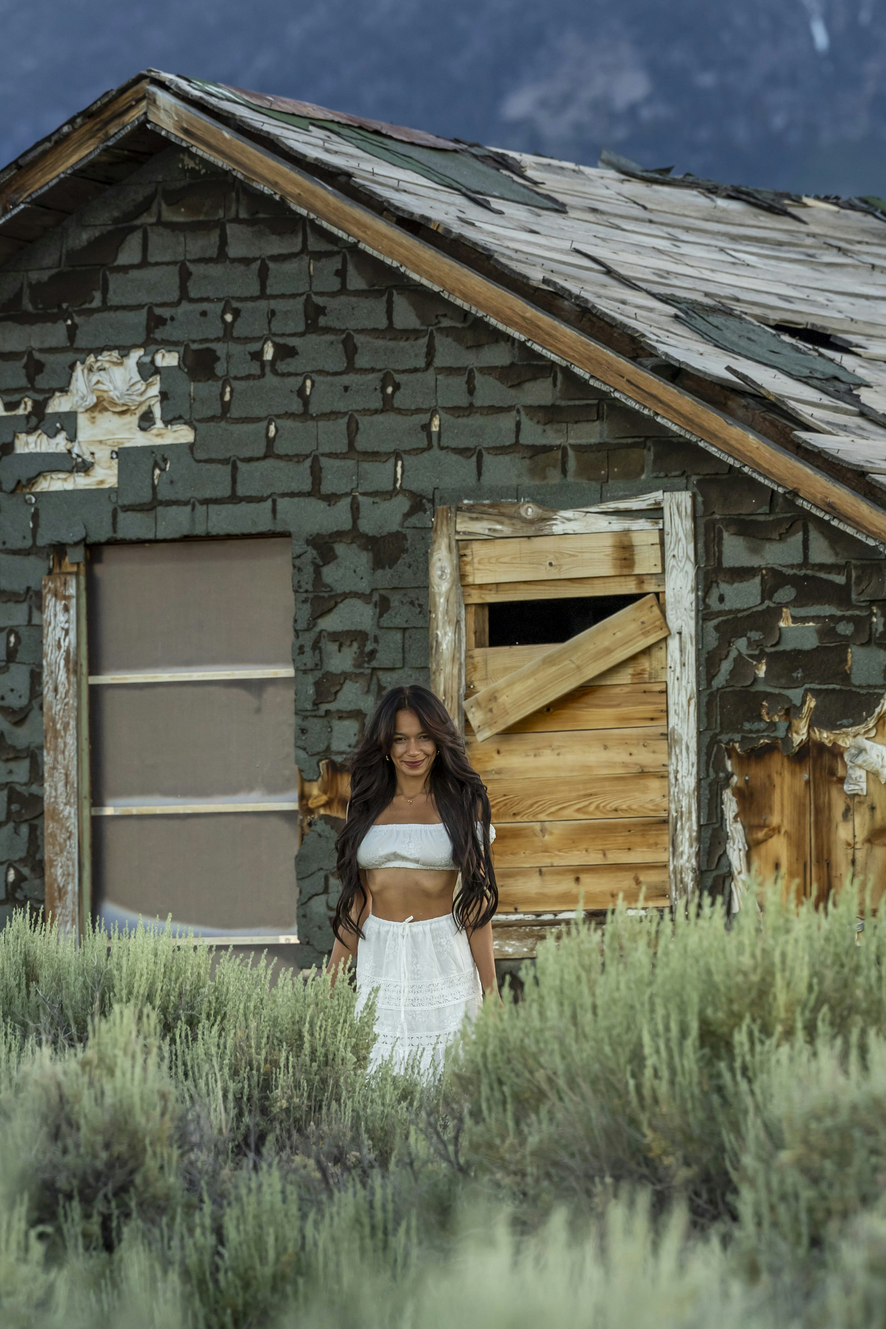 Girl in White Dress Stands Before Weathered Cabin Amid Sagebrush
