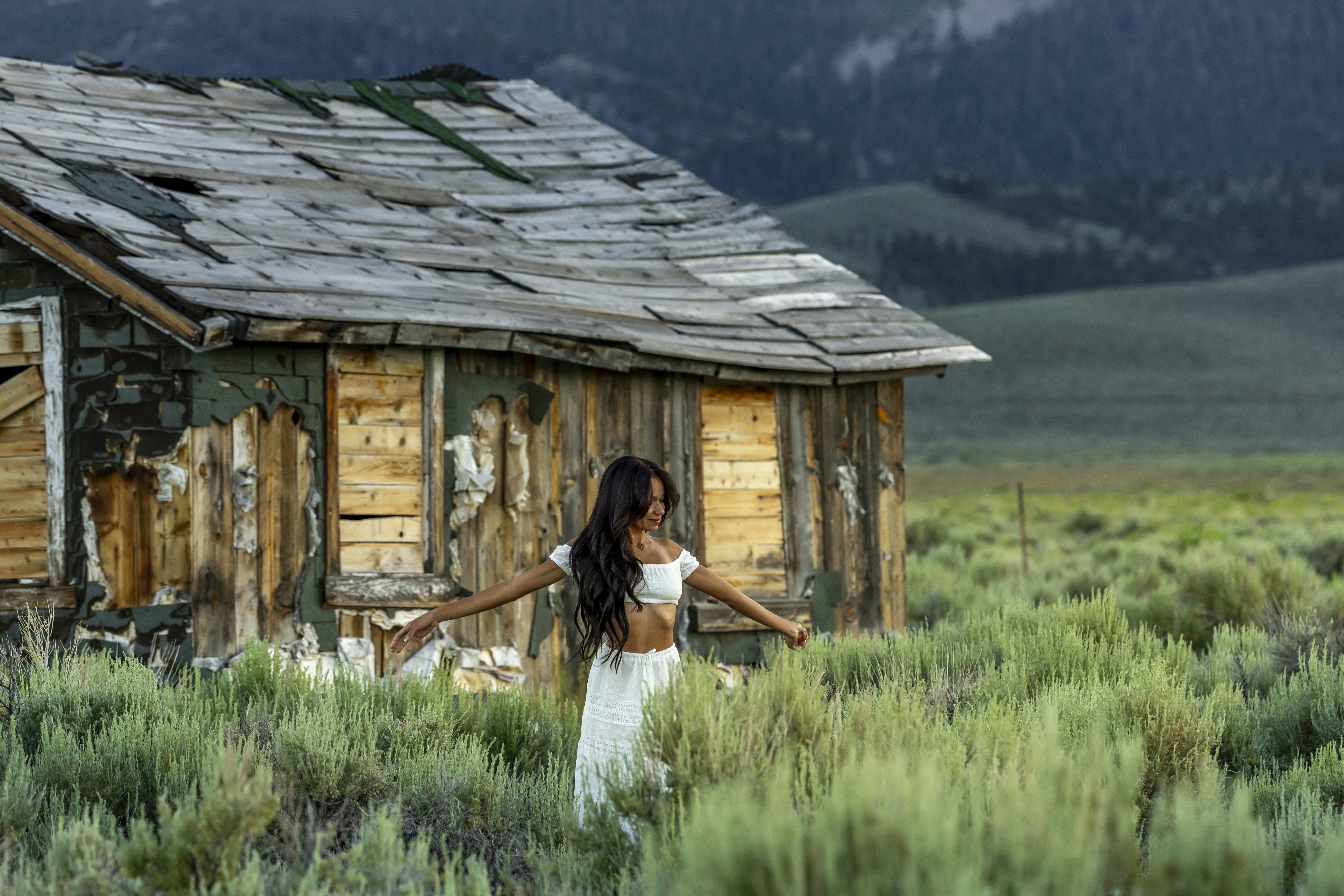 Woman in white stands at the edge of a weathered cabin in a lavender field