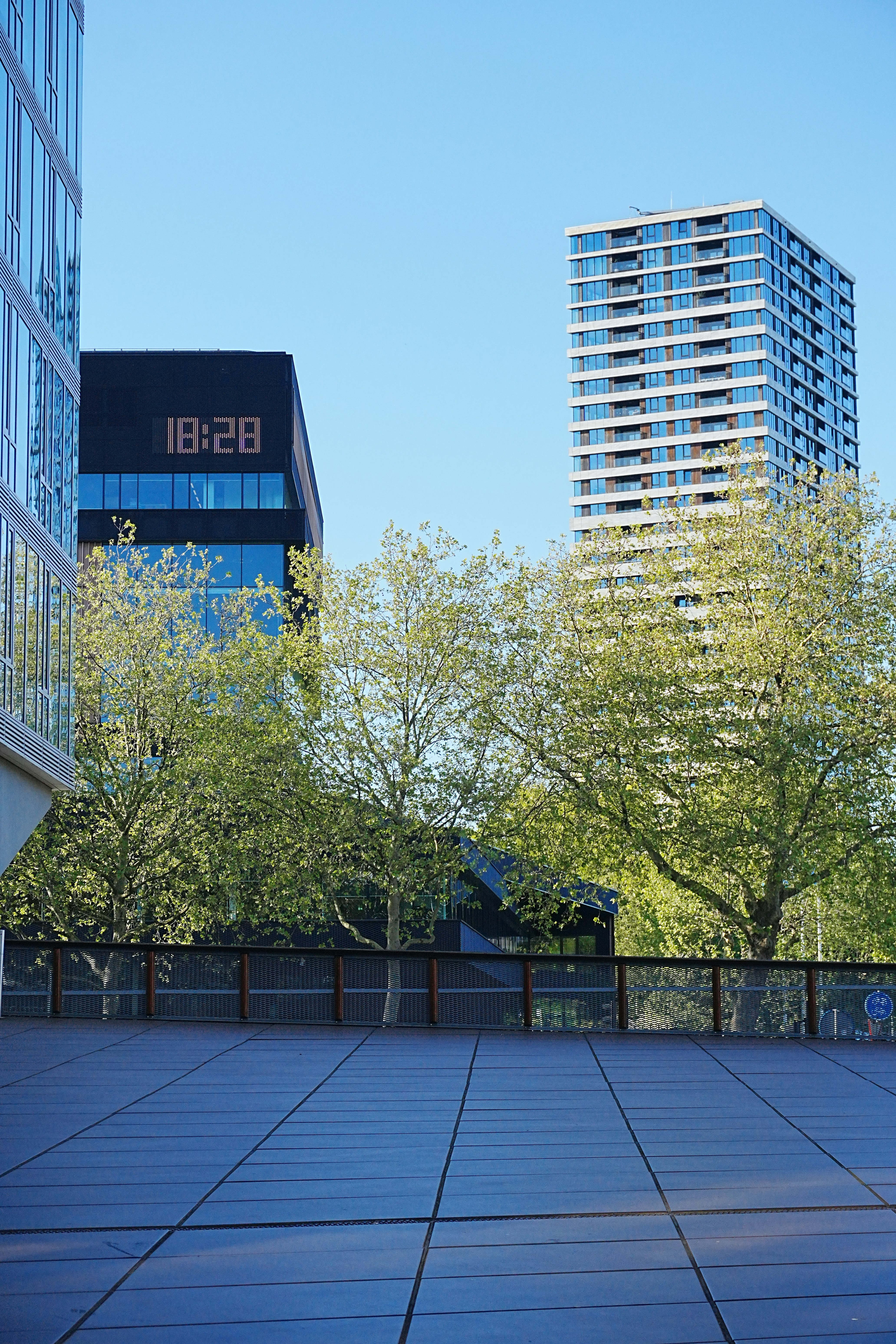 Morning Cityscape: Glass Towers & Green Canopy Framed by a Quiet Terrace