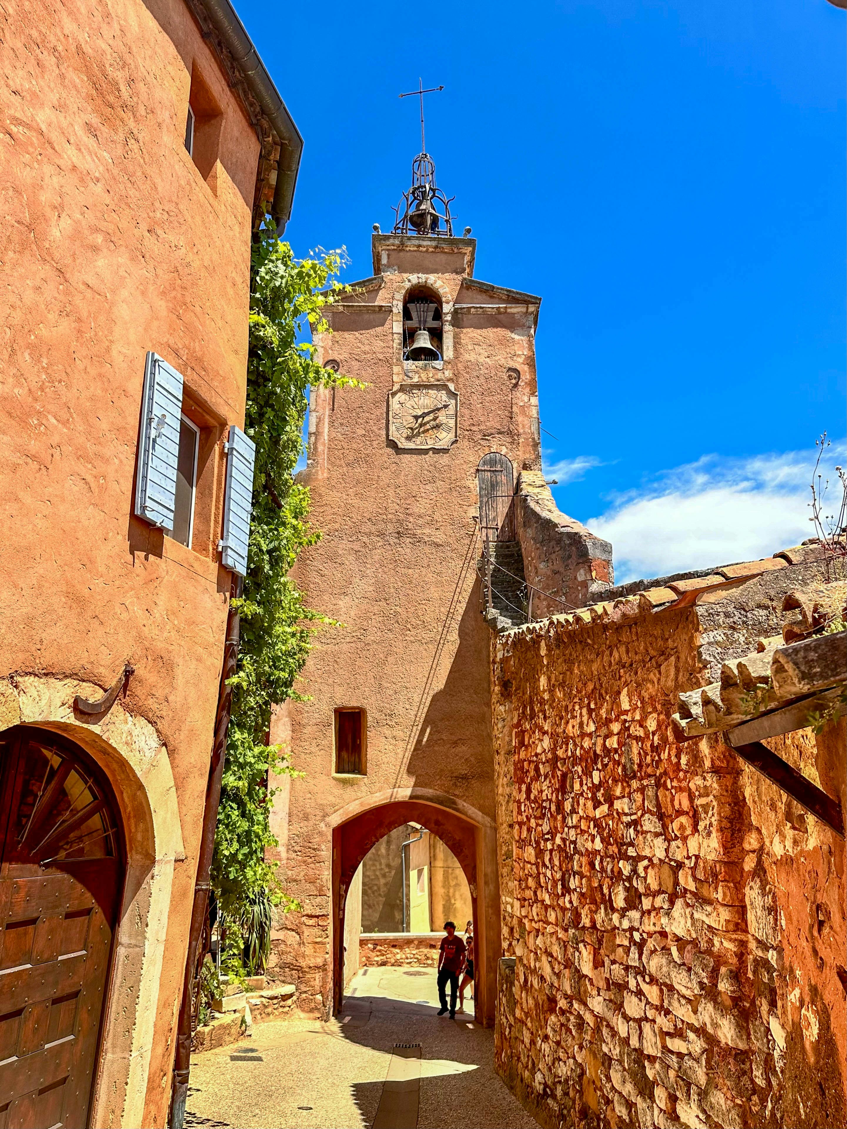 Sunlit plaza corridor beneath a rustic church tower