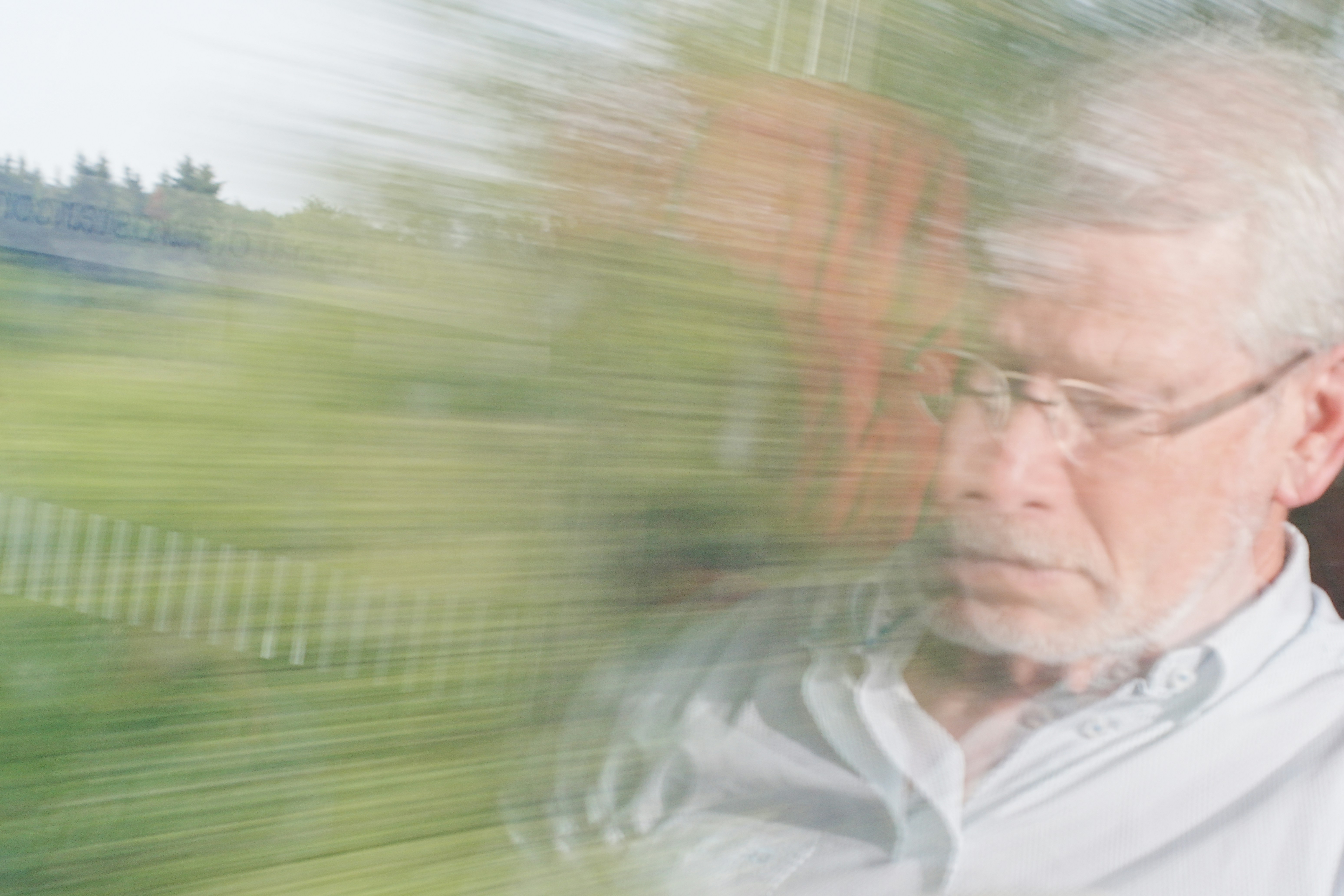Blurred portrait of an older man with glasses, seated indoors near a window, with motion streaks suggesting movement; appears as a shallowly blurred candid or deliberate motion effect.
