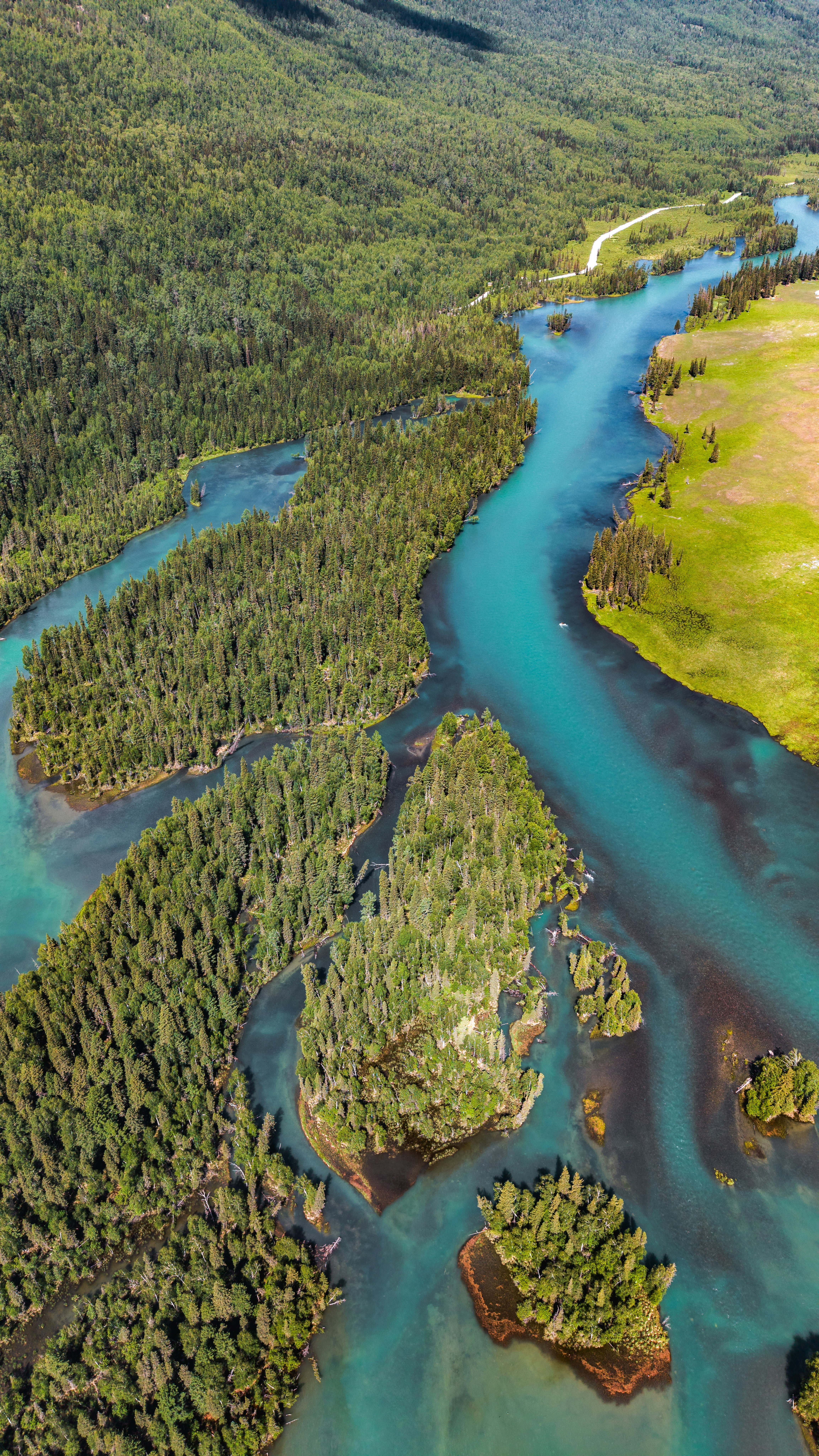 Winding turquoise river amidst green forests and small islands.