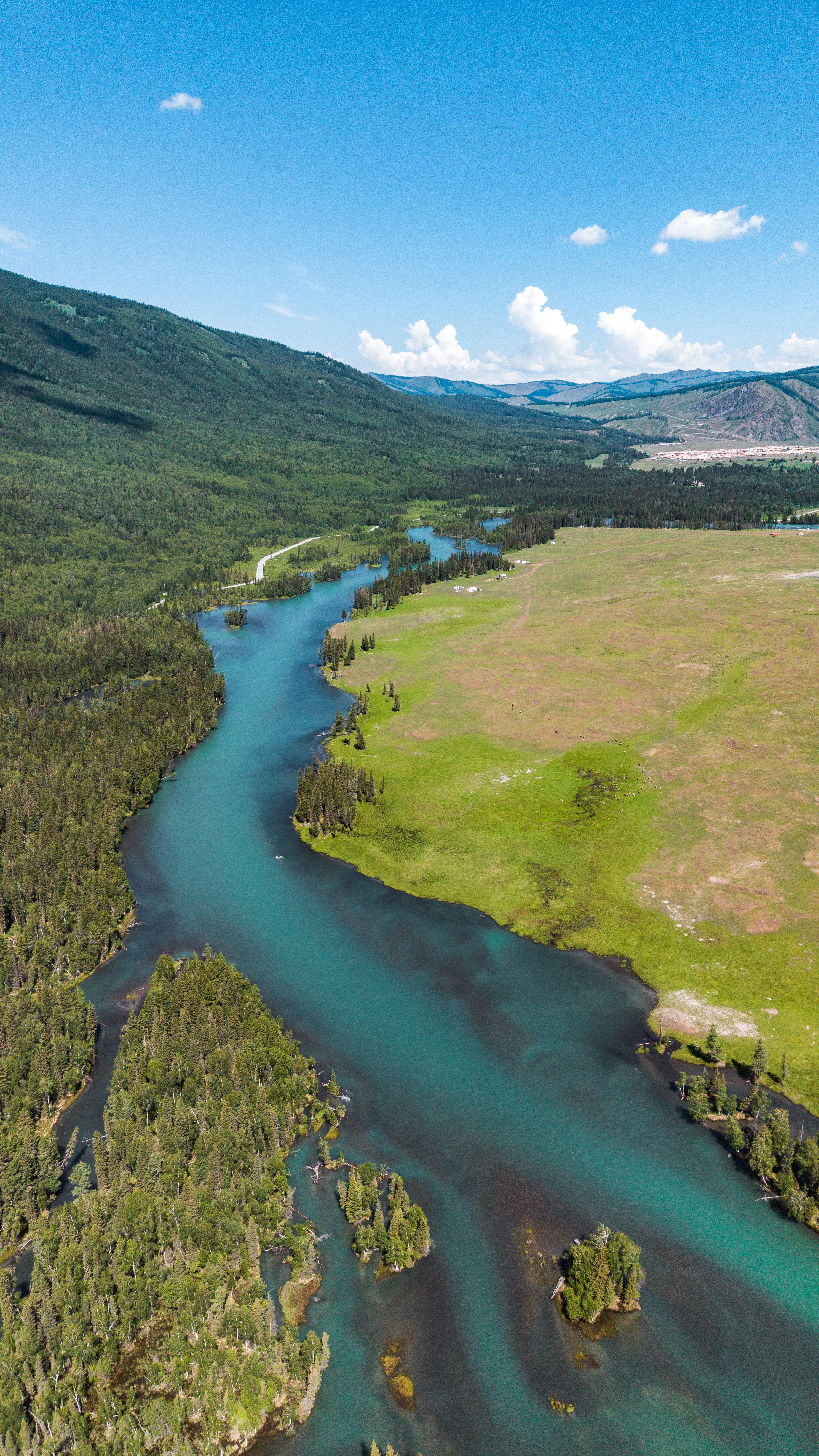 Wide river winds through a valley flanked by forests and open meadows, captured from above to reveal the turquoise water and surrounding landscape.