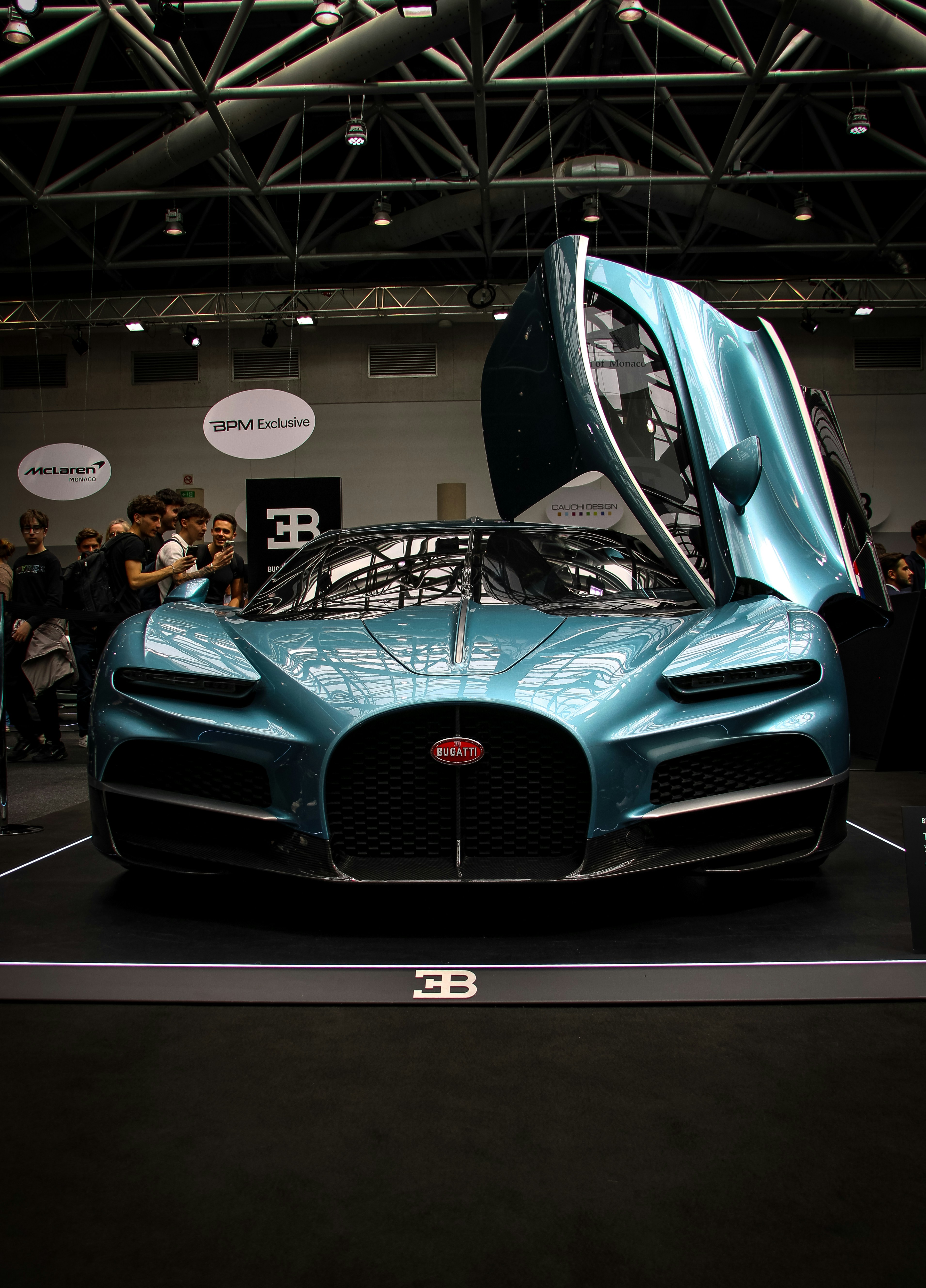 A turquoise Bugatti at the Forefront: Open Gullwing Door and Show Floor Spotlight