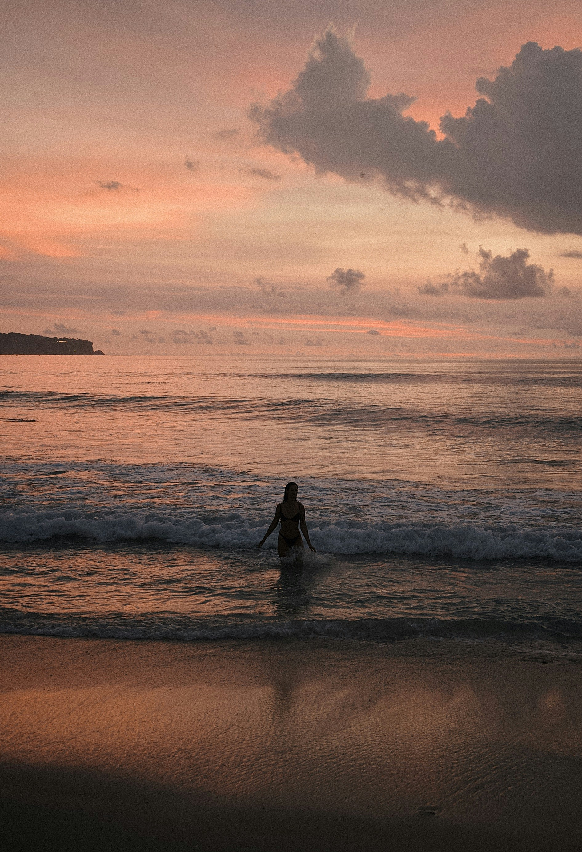 Sunset Silhouette: A Figure Wading into Coral-Hued Waves