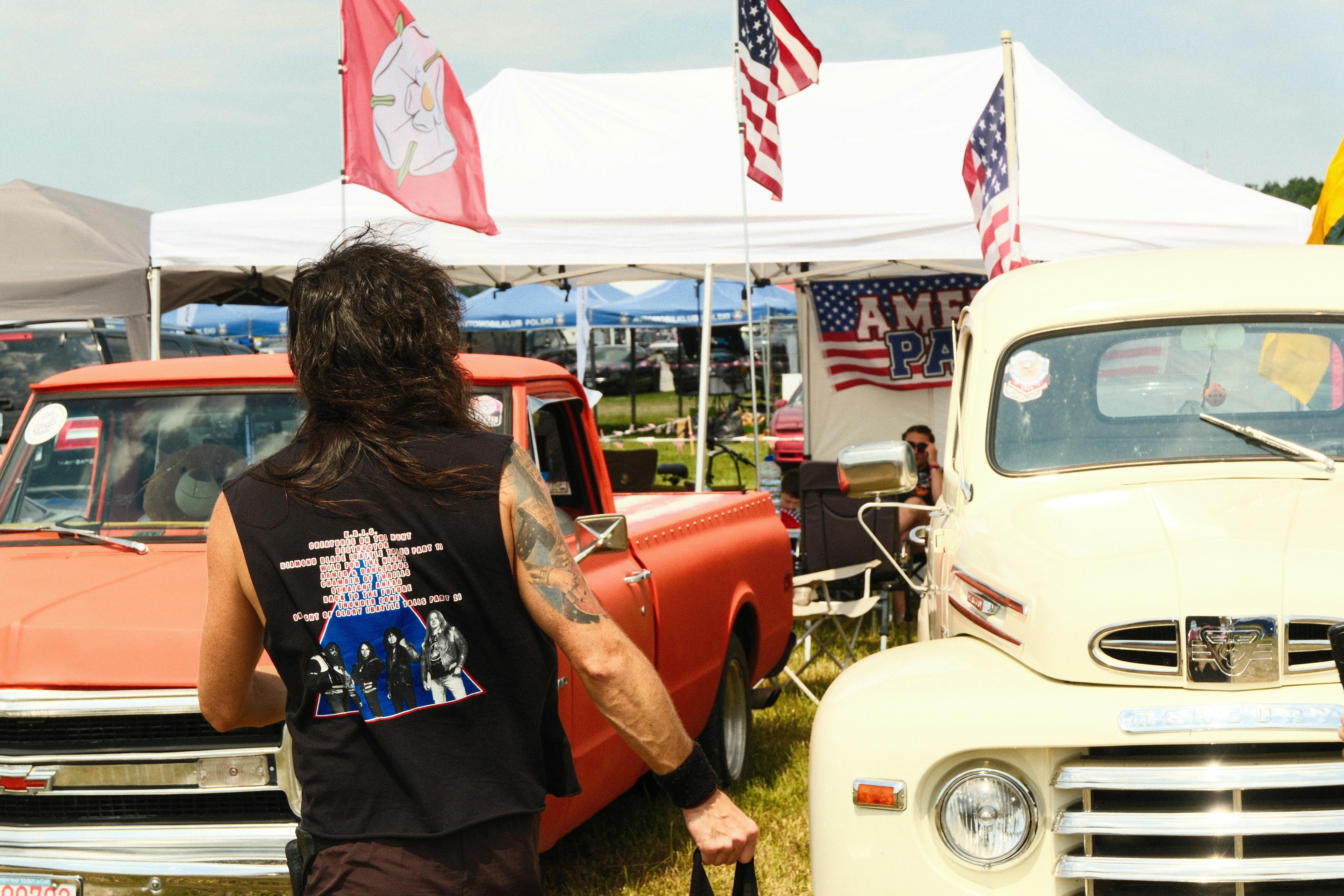 Backstage at the Car Show: A Tattooed Observer in Steel and Flags
