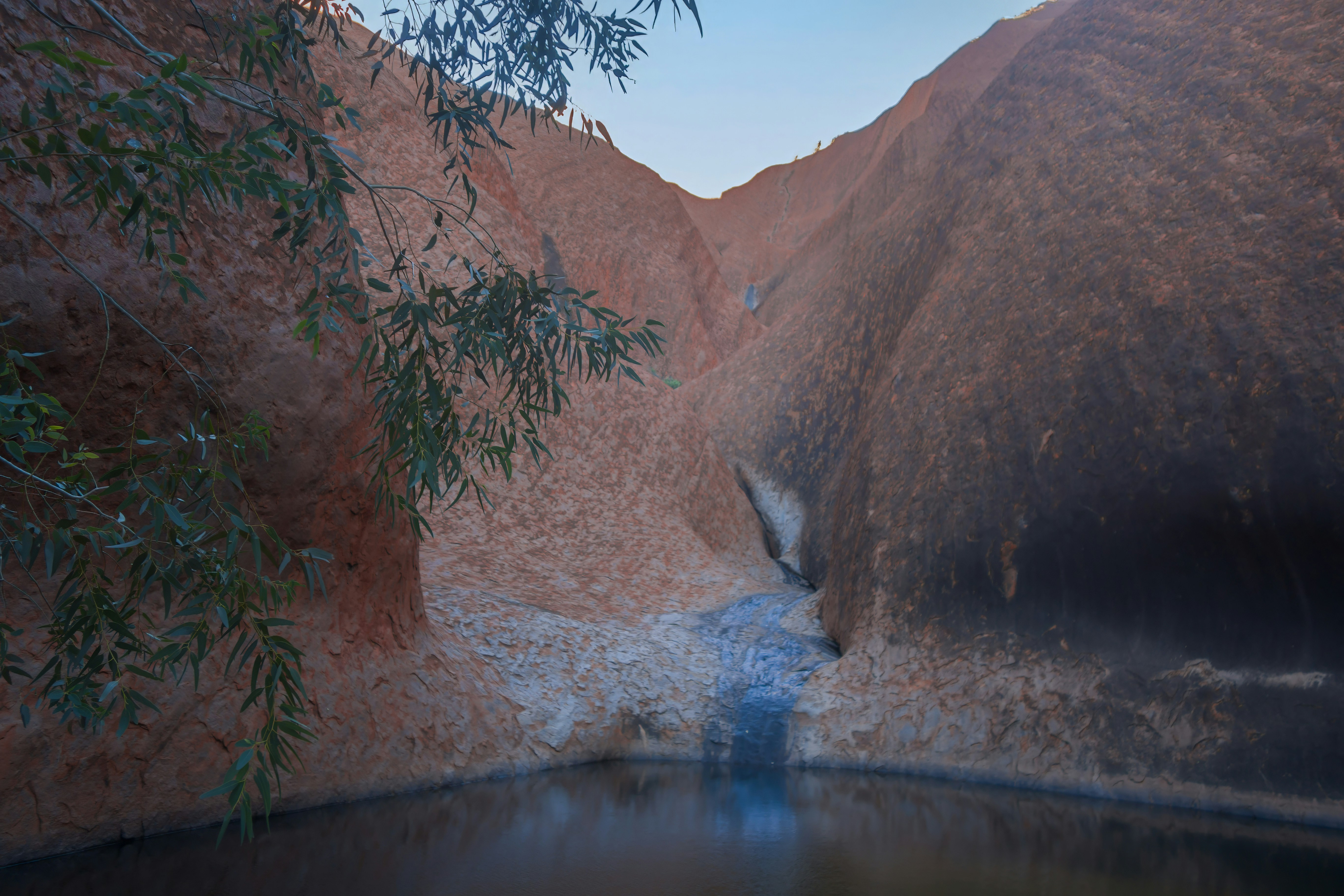 Small waterfall cascades into a serene pool amidst red rocks.