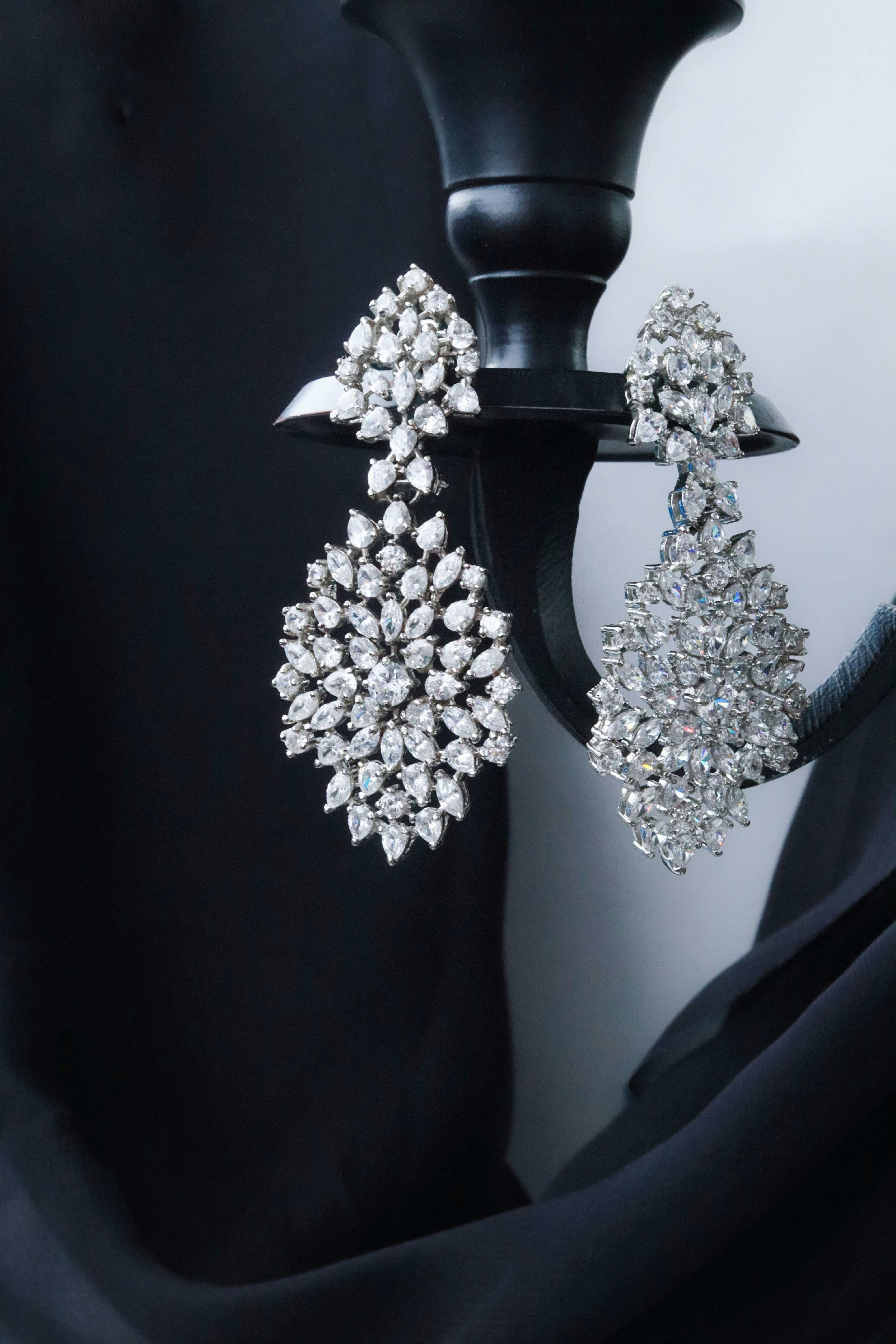 Elegant diamond-embellished earrings displayed on a black velvet bust, catching light to reveal intricate pear and marquise-cut facets.