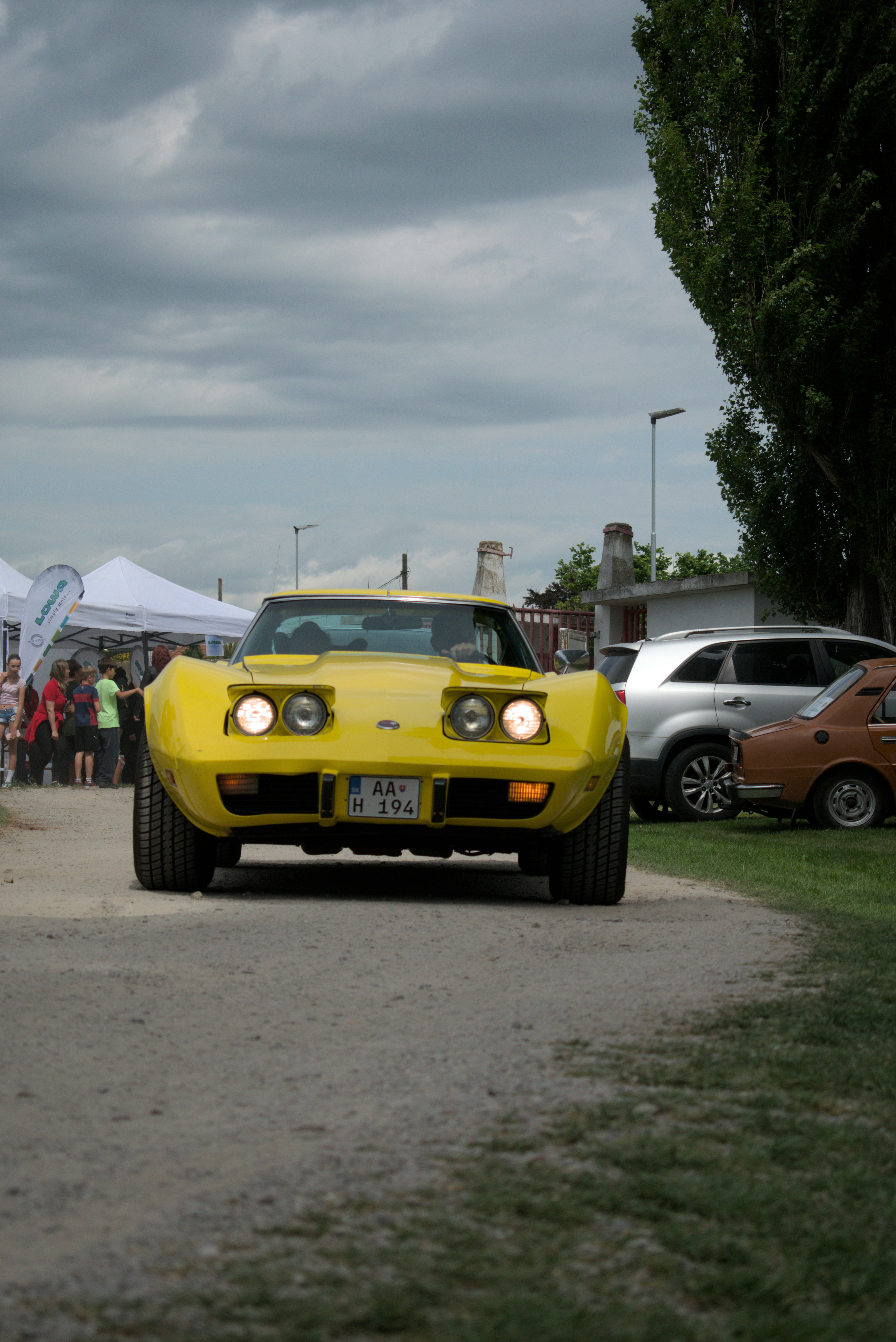 Yellow Muscle Car Leading the Crowd on a Gravel Road