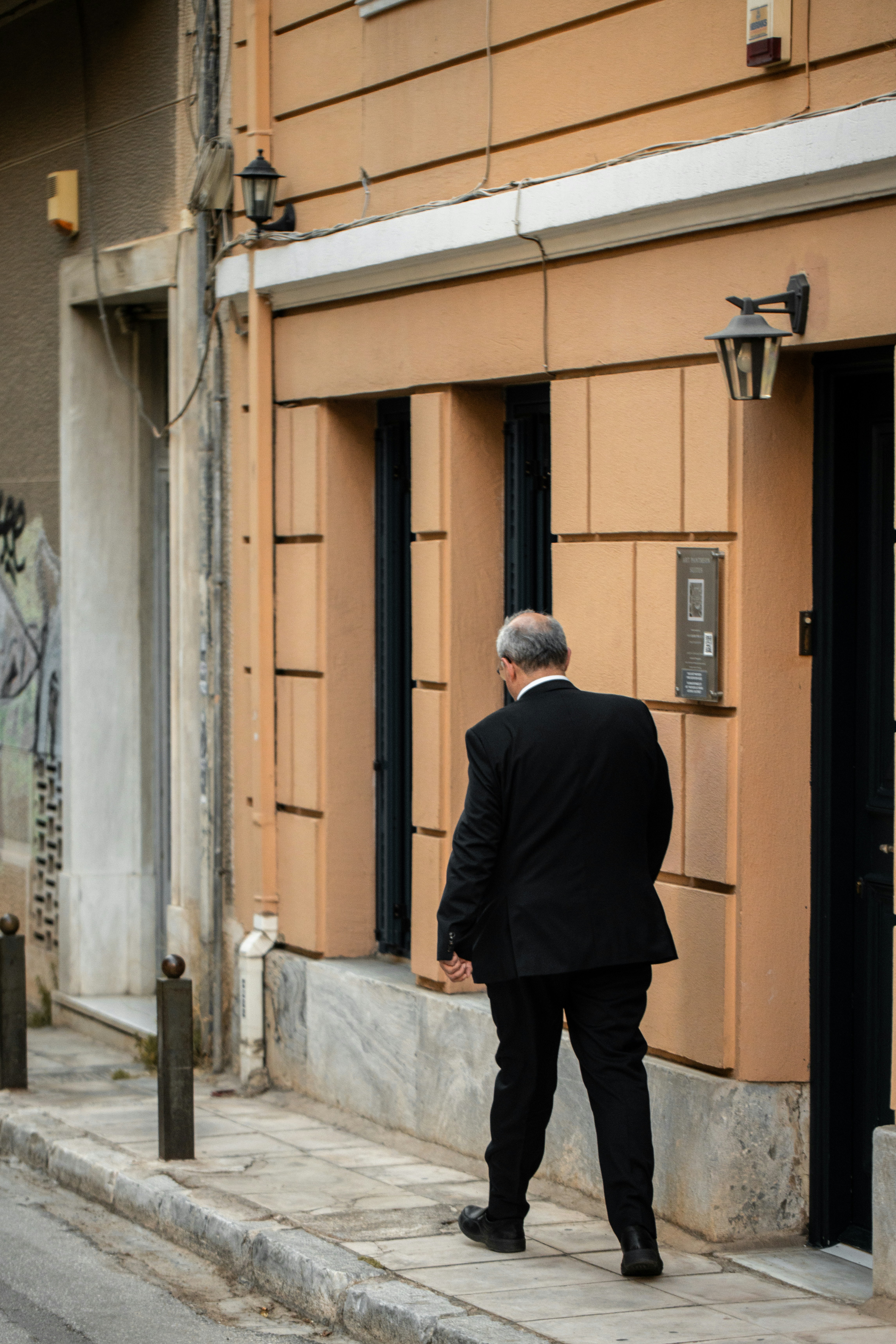 A Quiet Lesson in Silence: A Gentleman in a Black Suit Along a Peach Facade