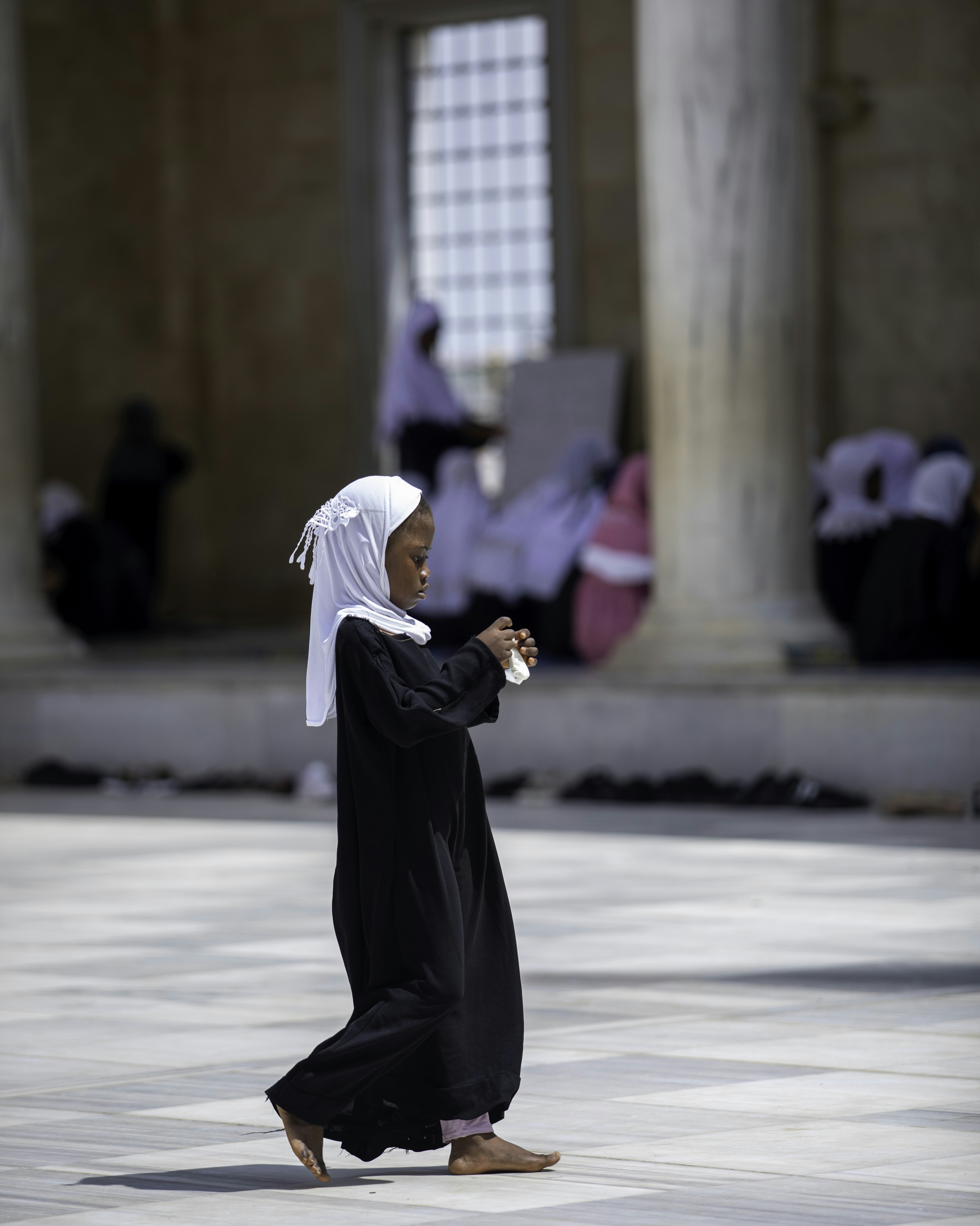 Child in a hijab walking barefoot inside a sunlit courtyard