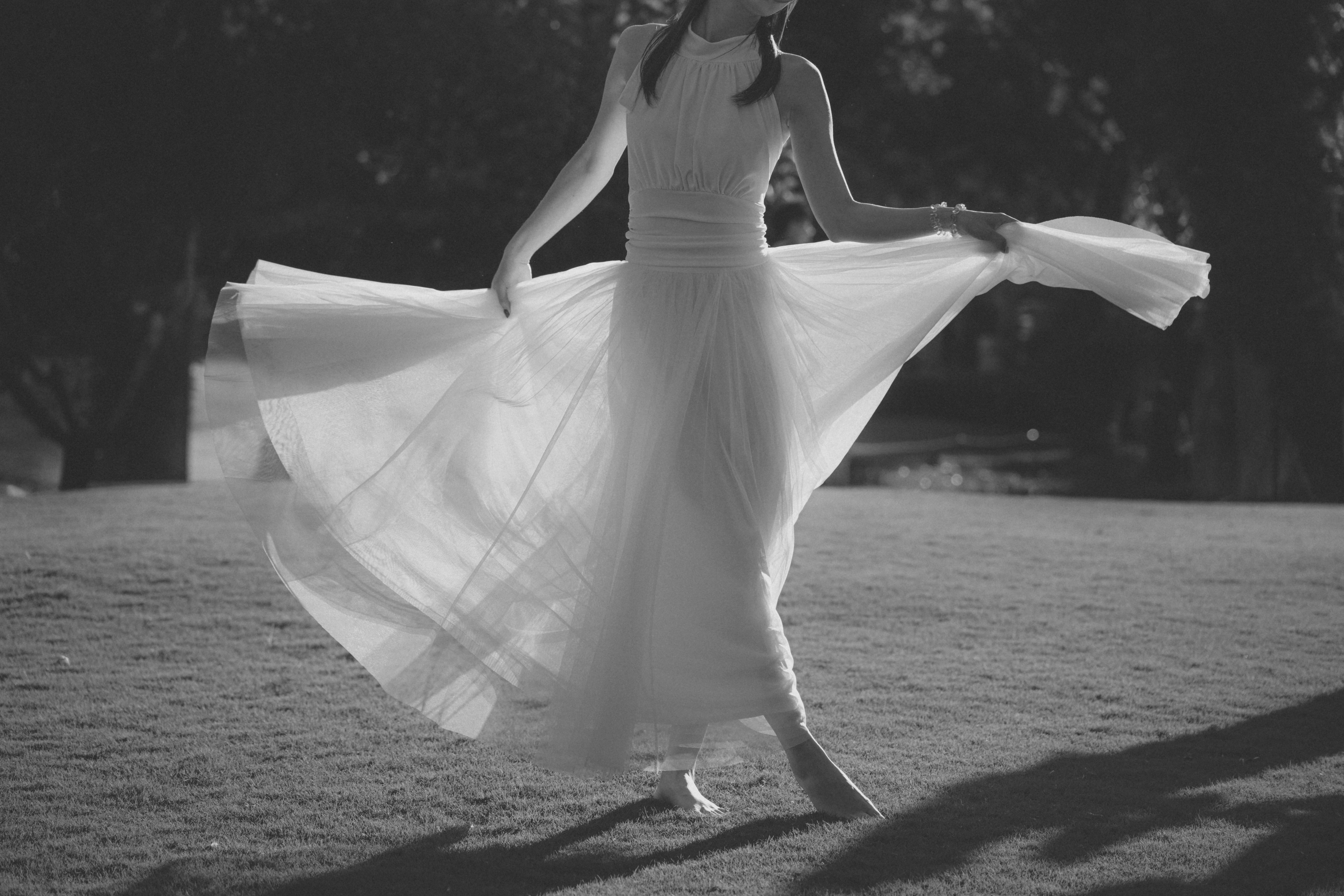 Barefoot woman twirling in a light dress on grass.