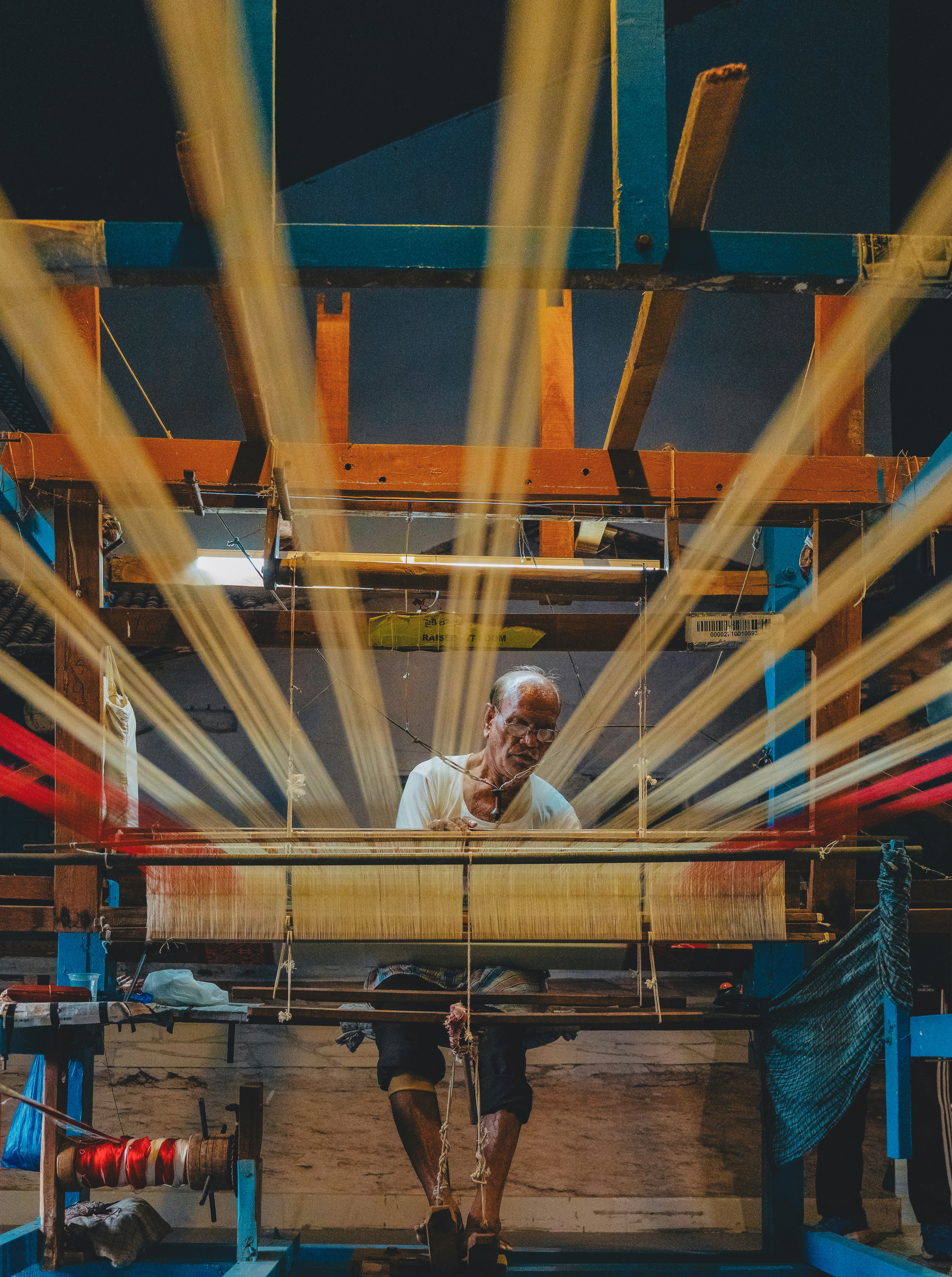 Threads Alight: A Weaver at the Loom Under Painted Beams