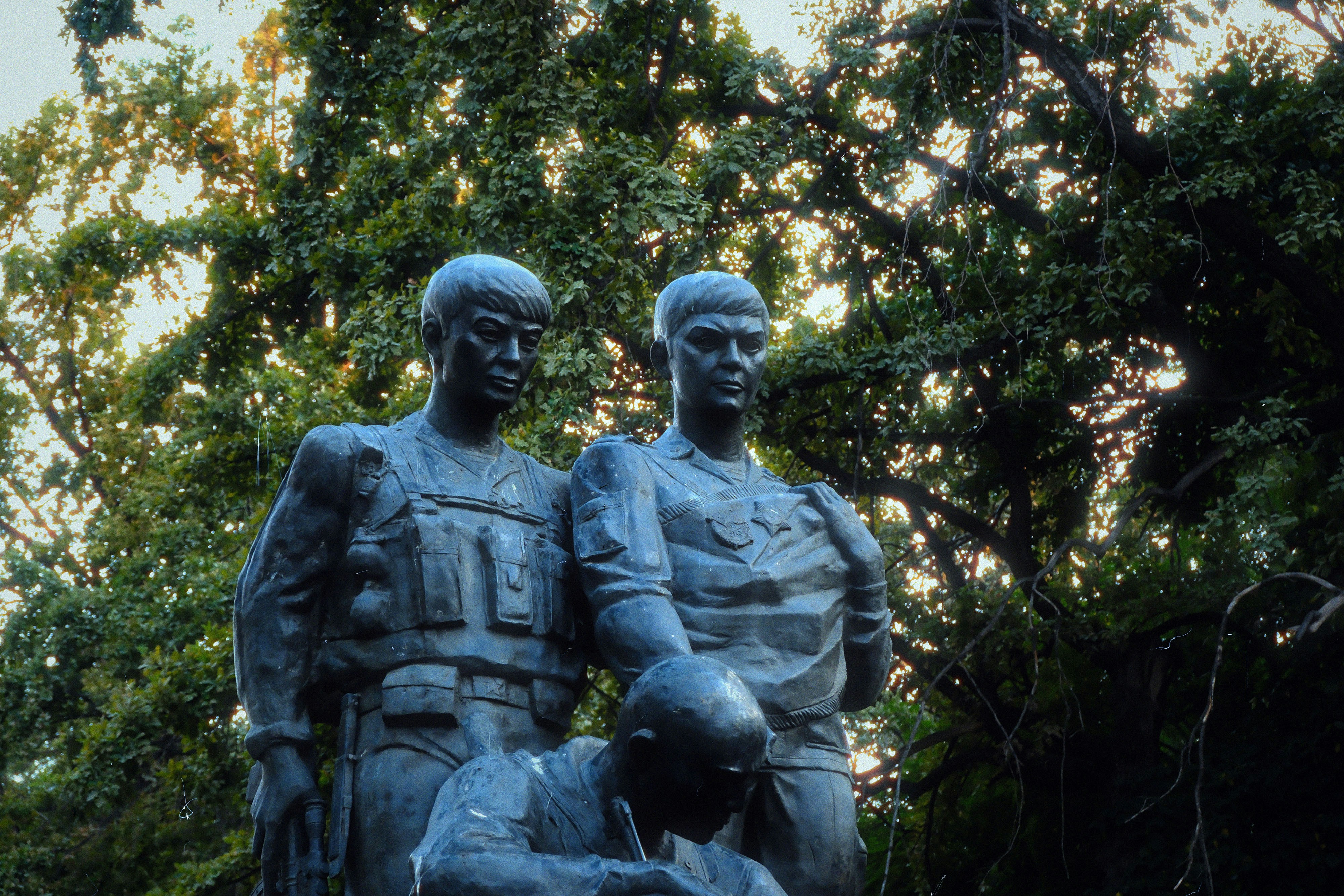 Guardians in bronze: a triad of soldiers under leafy dusk