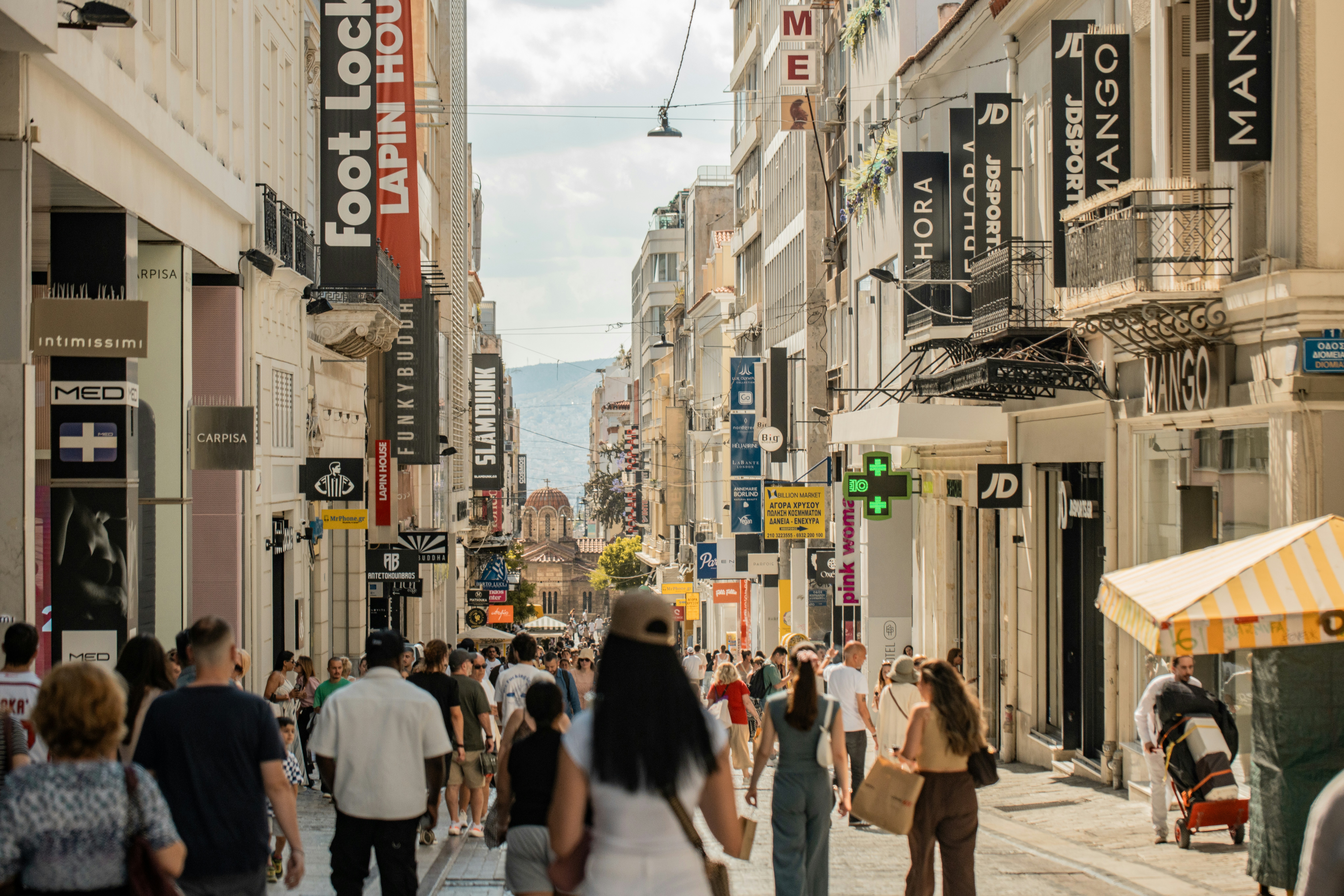 Bustling pedestrian street with signage-lined storefronts and sunlit crowd