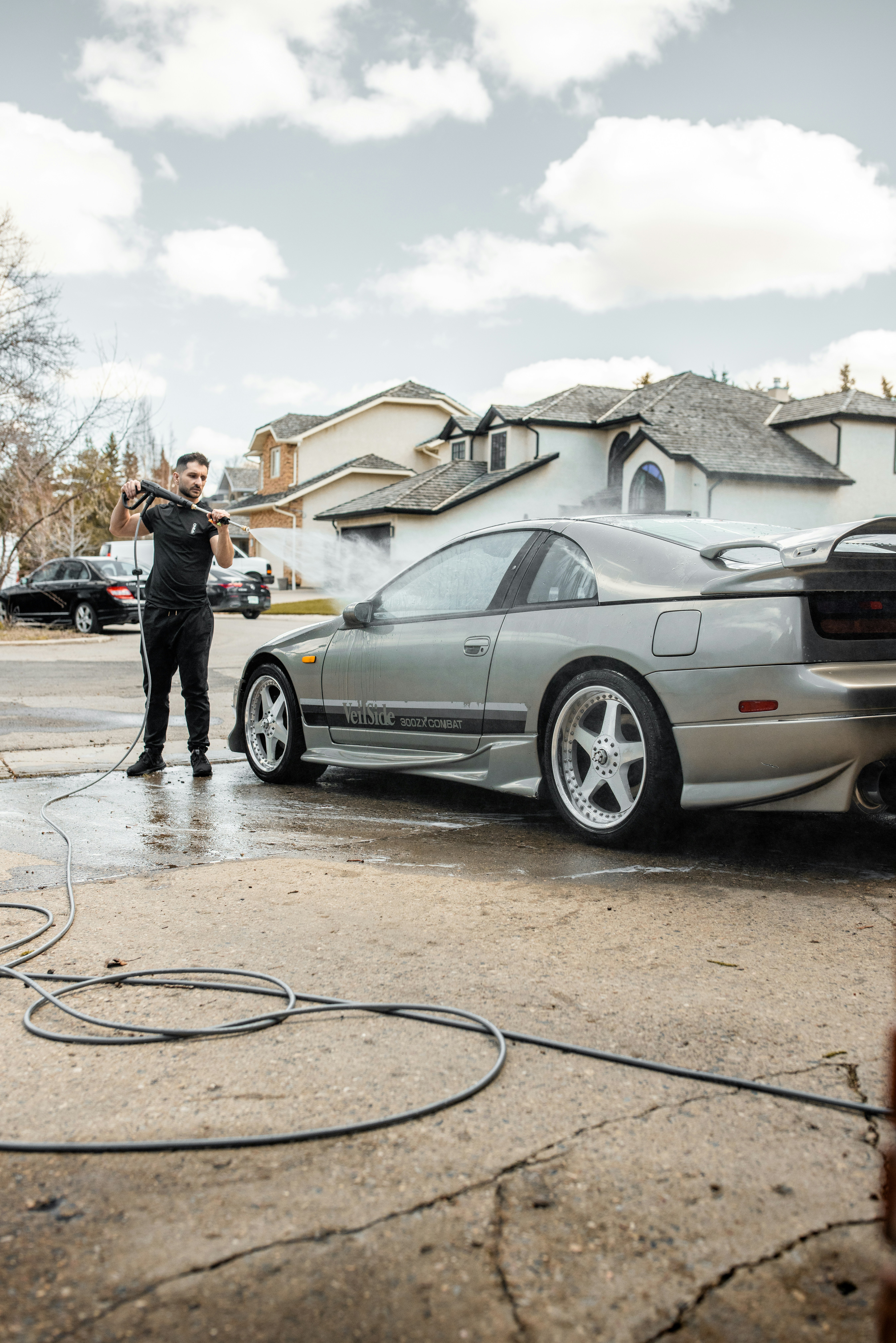 Car Wash in Action: A Groomed Silver Ride and the Enthusiast with a Hose