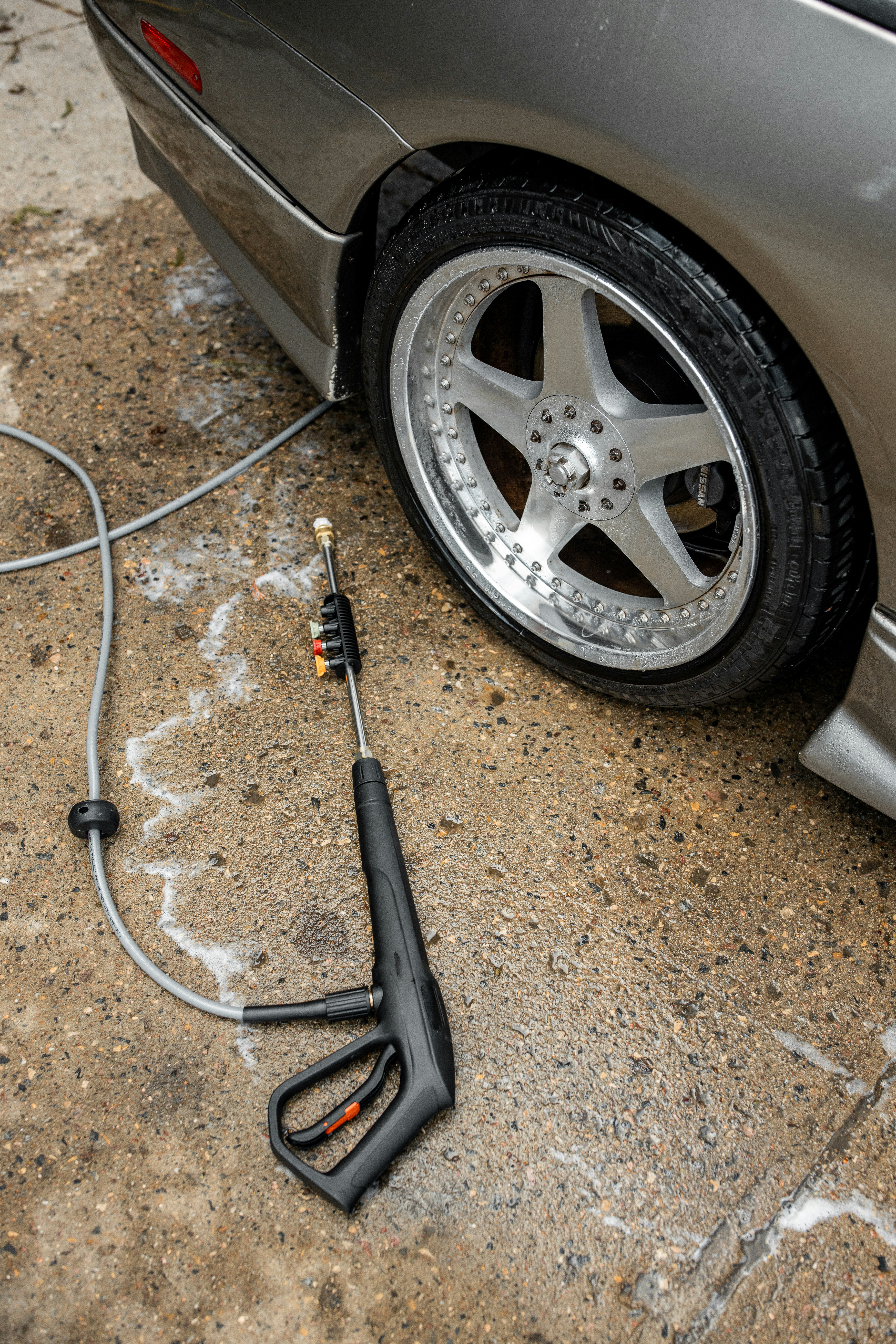 Low-Angle Car Wash: A Silver Wheel and Pressure Washer in Focus