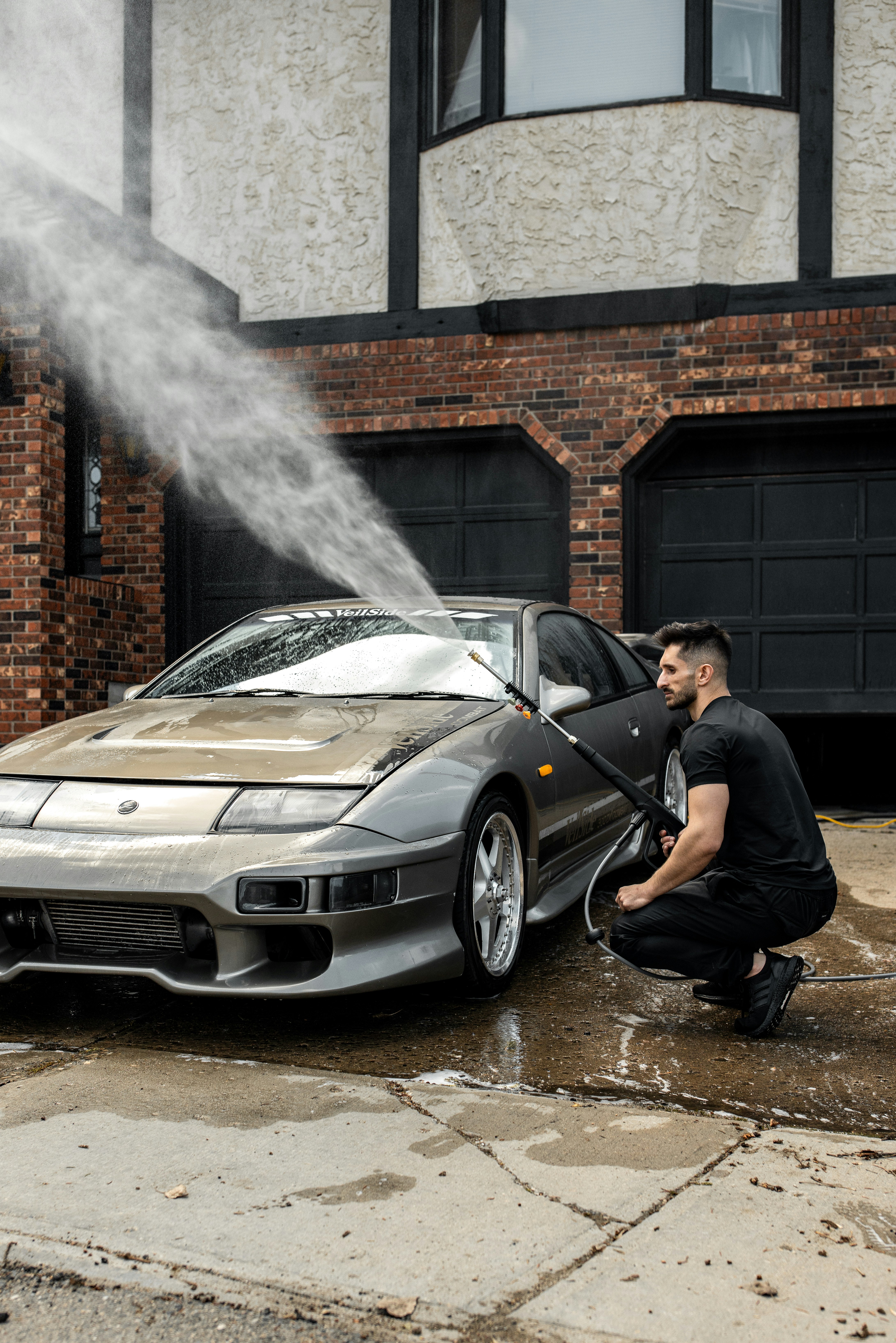 Powerwash in Progress: A Man Directs a Car Wash Spray at a Silver Sports Coupe