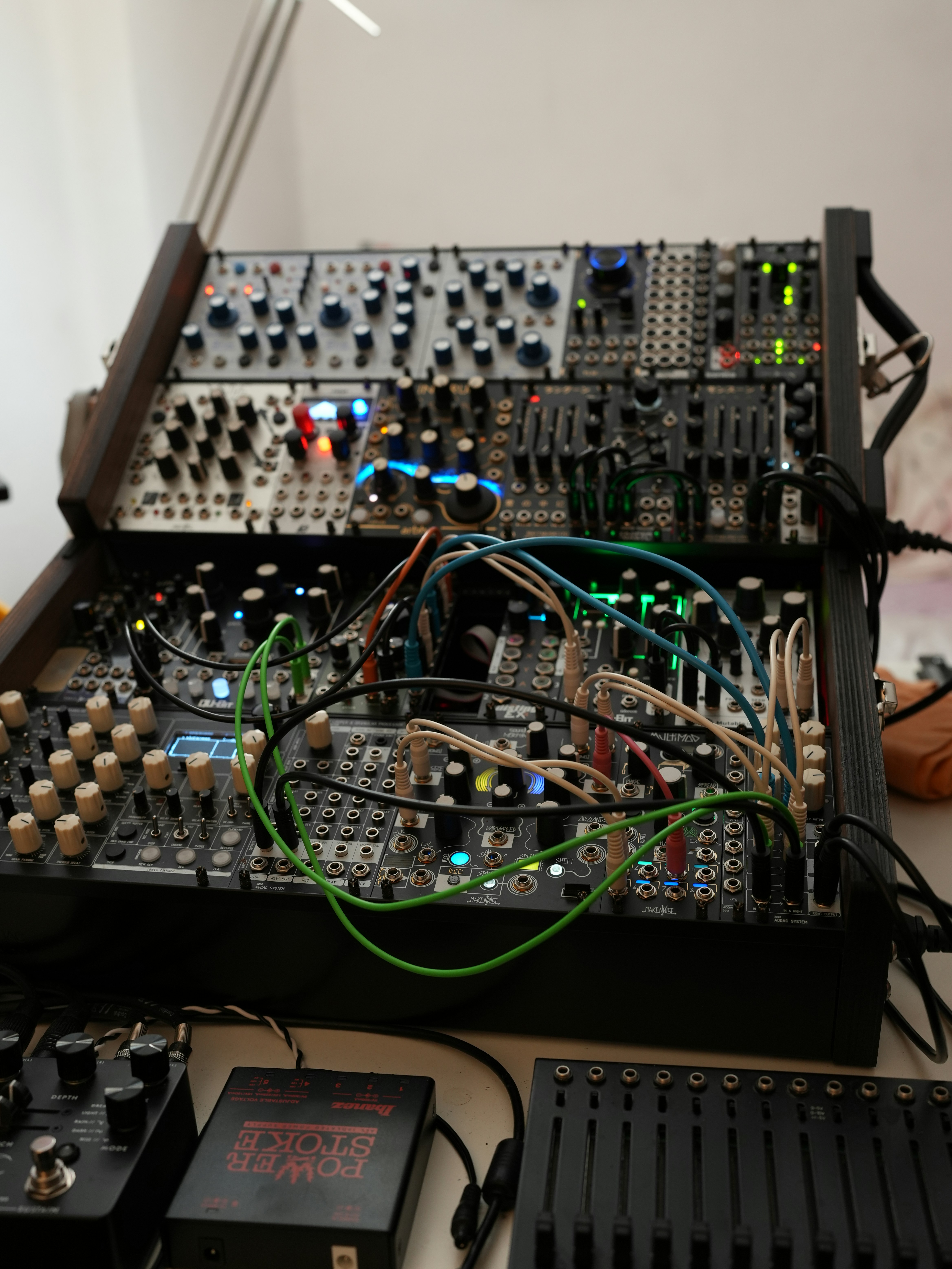 Close-up of a modular synthesizer rack with numerous cables and controls, showcasing a complex patch in a dimly lit studio setup.