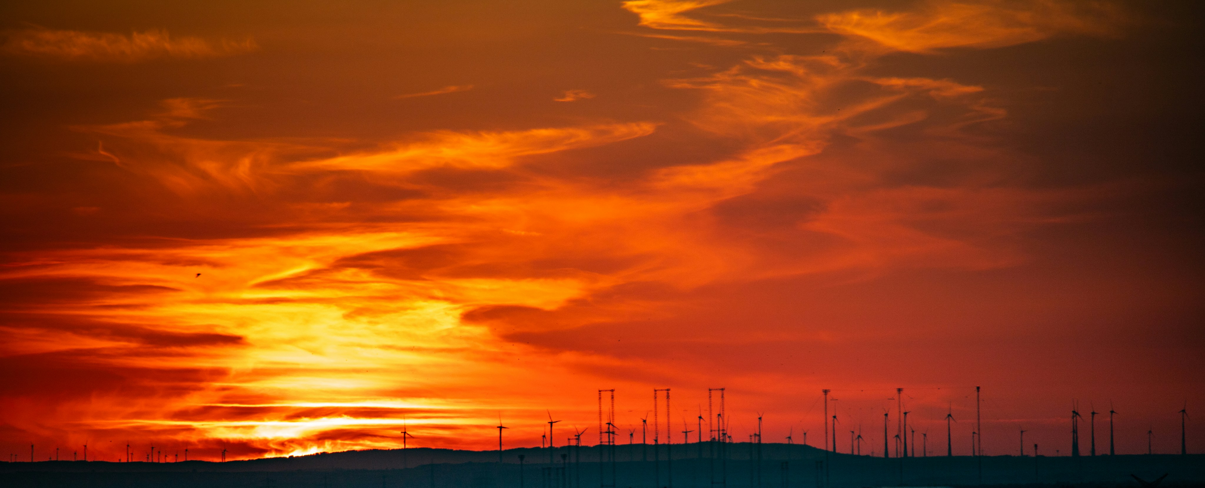 Sunset on the Skyline: Distant Wind Turbines Silhouetted Against Fiery Horizon