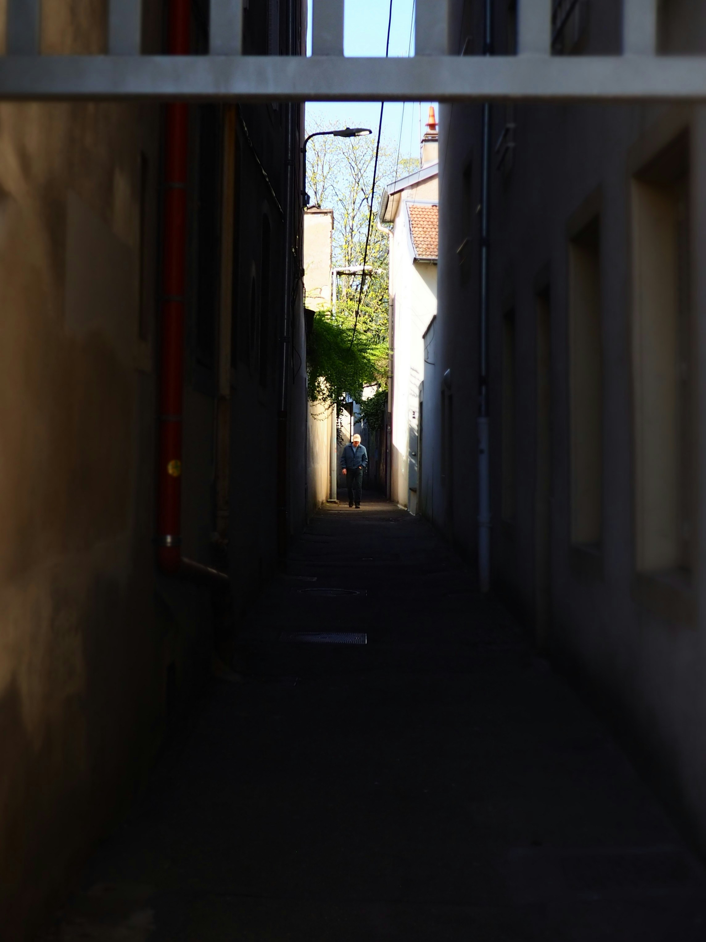 Narrow alleyway leads to a distant figure bathed in daylight