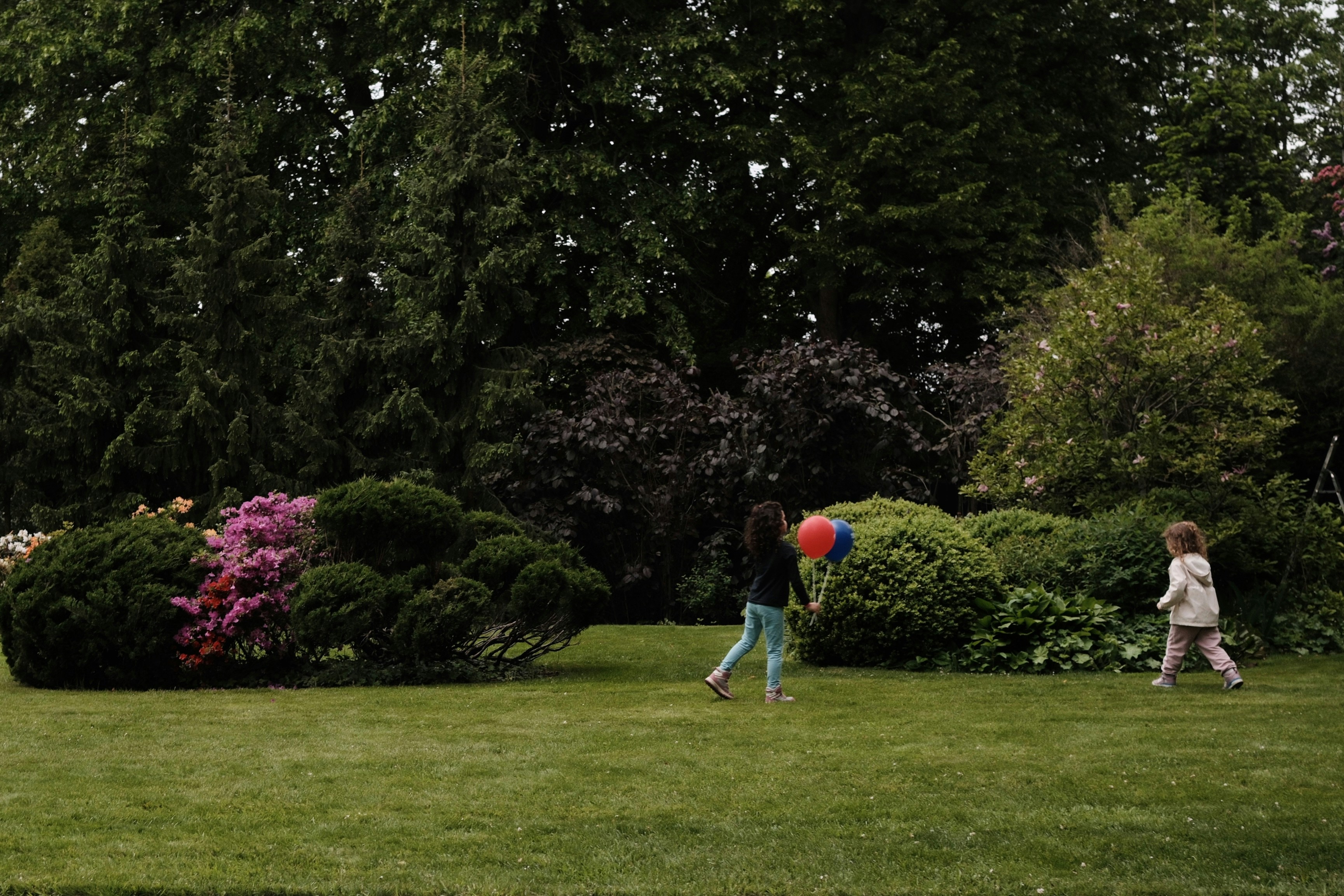 Two Children Chase Balloons Through a Quiet Park