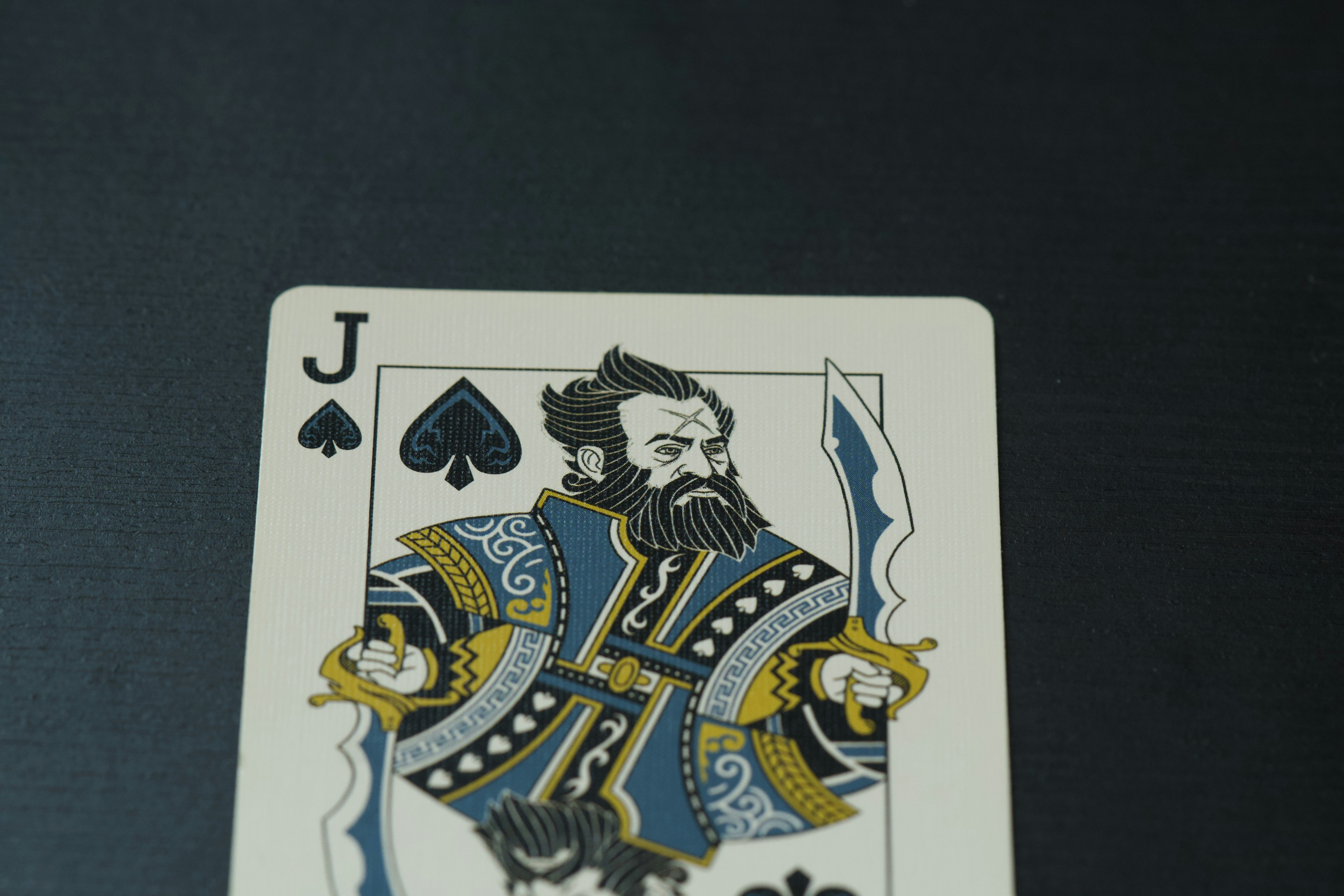 Close-up of a King of Spades playing card displayed against a dark background, featuring ornate blue and gold detailing and a bearded figure. (Note: This is a playing card, not a logo or illustration.)