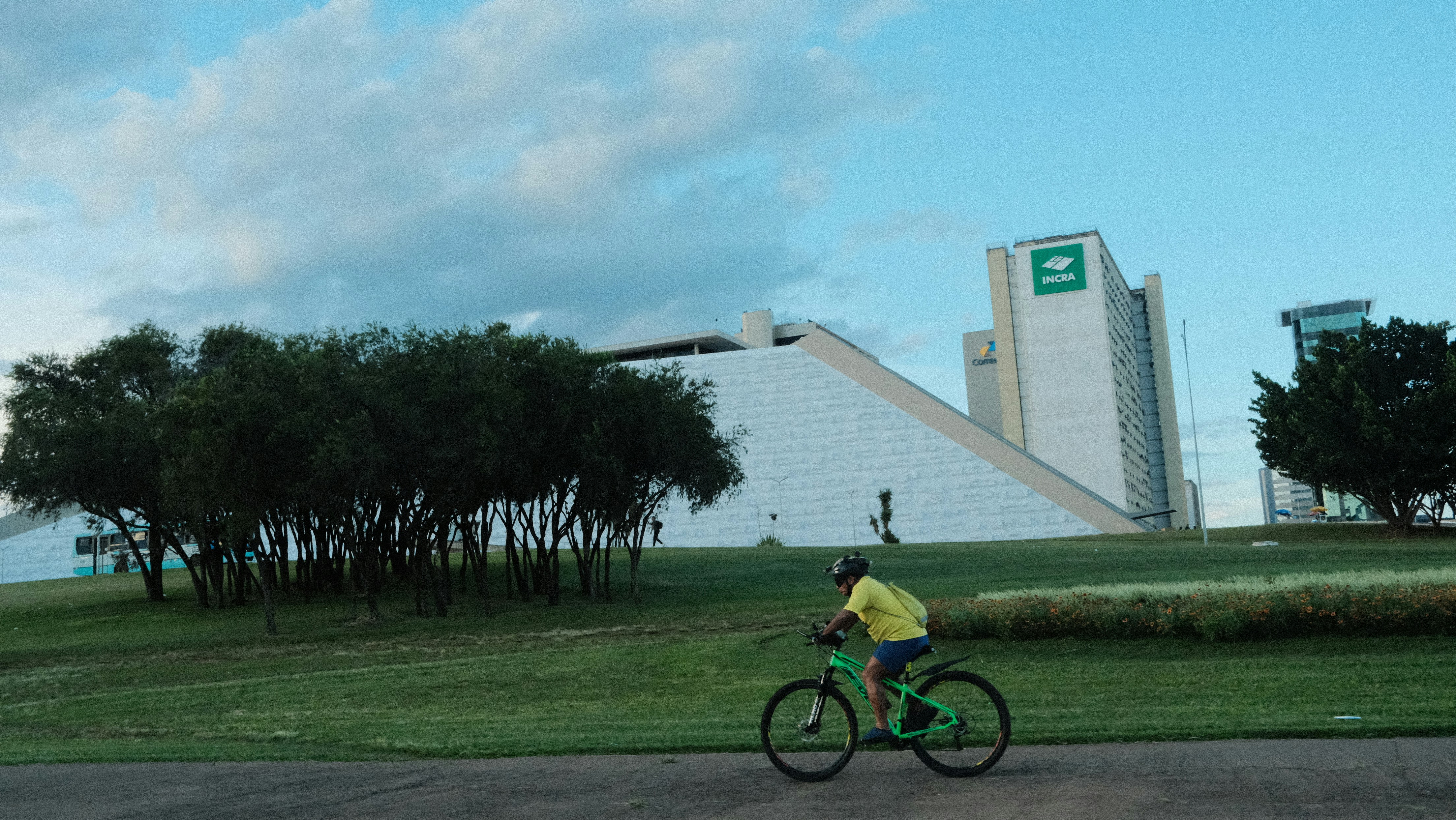 Solo cyclist on a sunny park path with modern campus architecture looming in the background