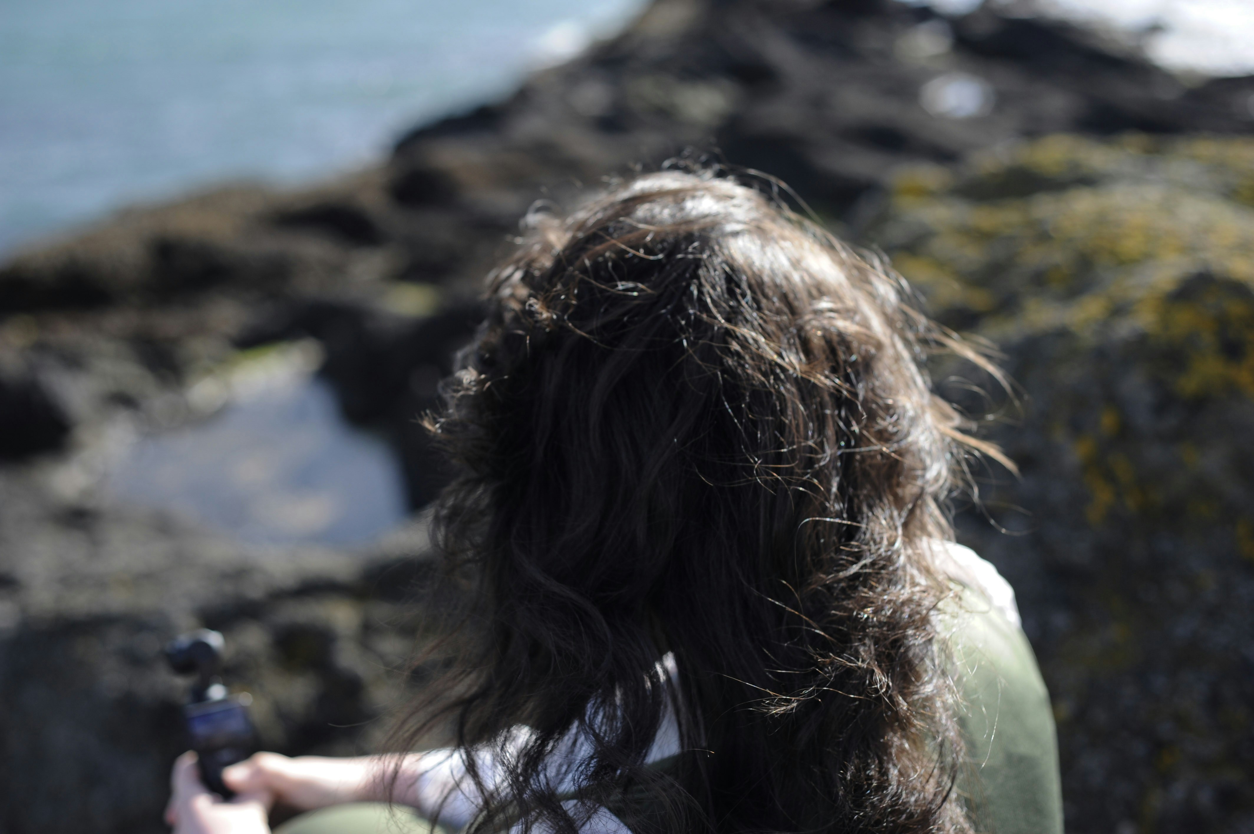 Bokeh of Sea Breeze: Figure with Backturned Hair Amid Coastal Rocks