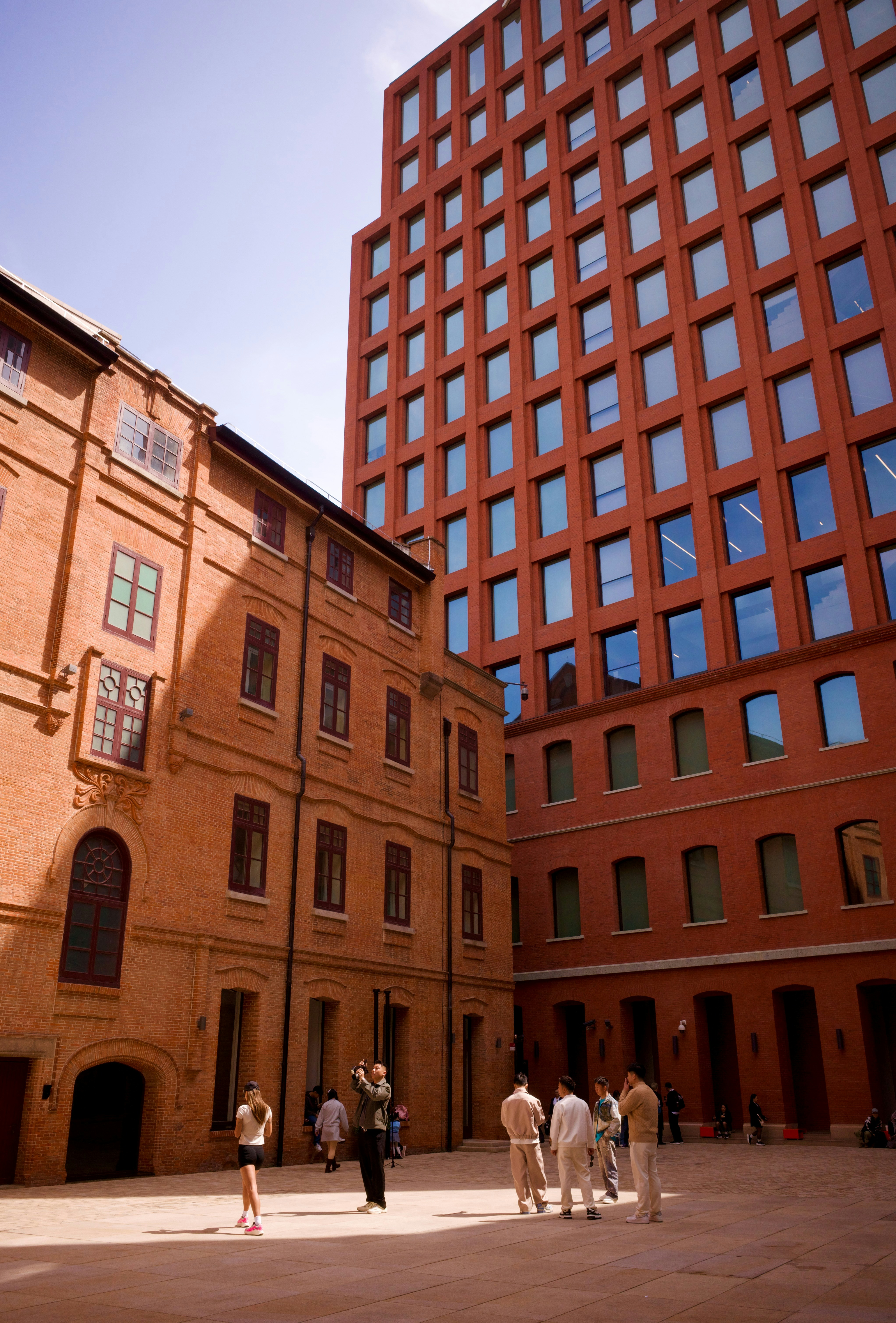 Courtyard Between Brick Facades: People in Soft Shadow under Red-Grided Sky