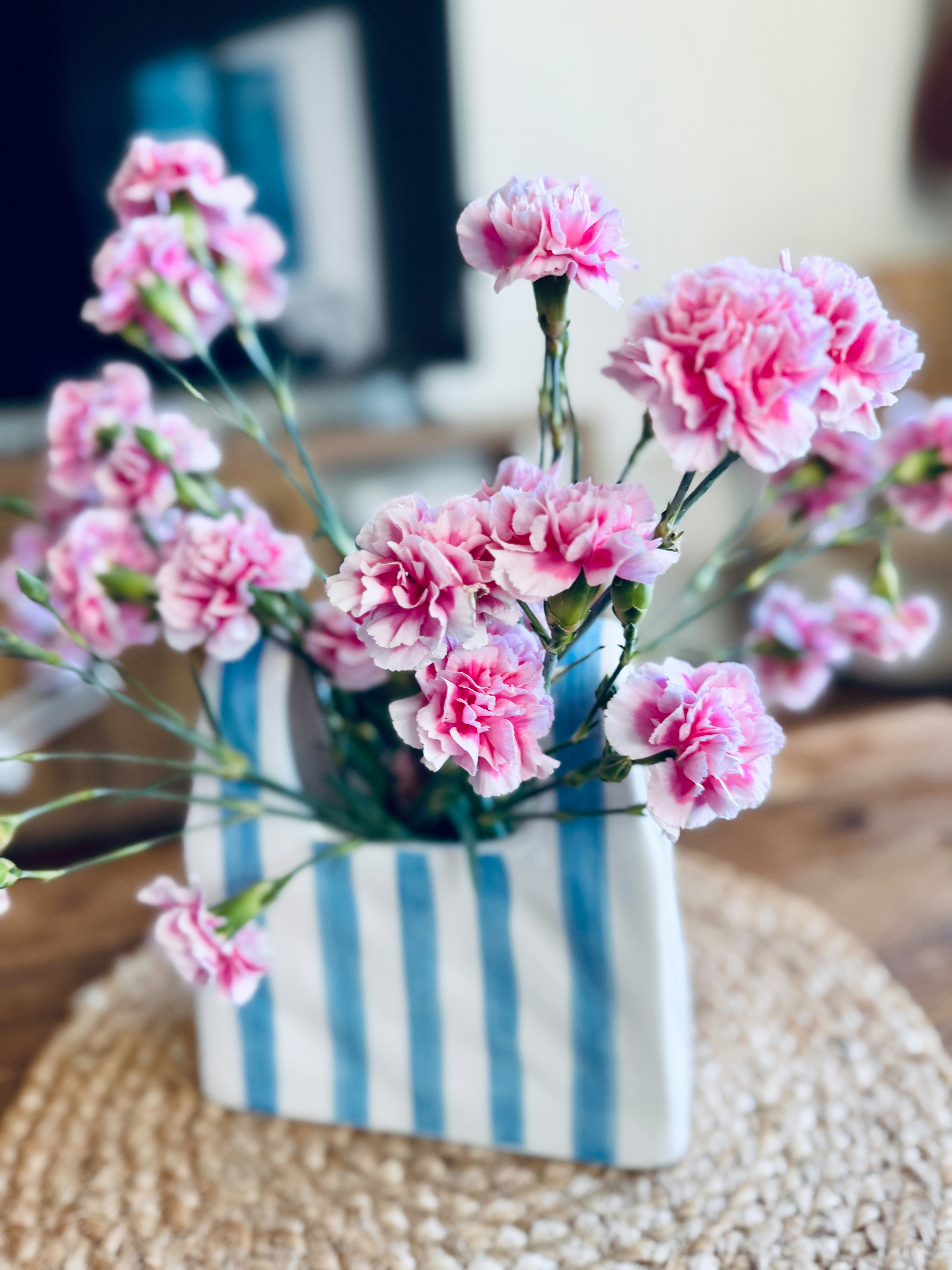 Pink Carnations in a Striped Ceramic Vase on a Rustic Mat