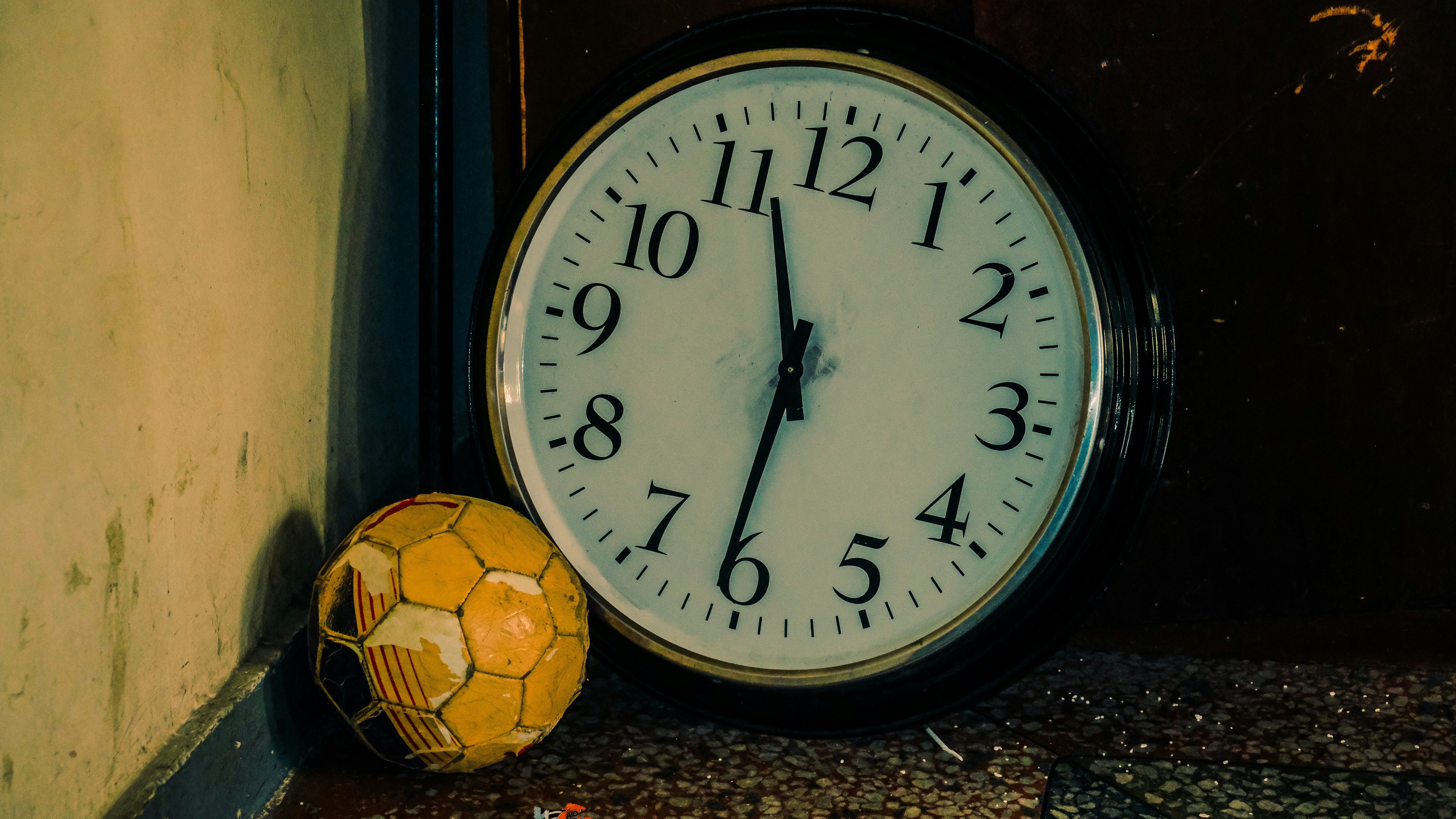 Time Stalled: A Weathered Clock Leaning Over a Worn Soccer Ball