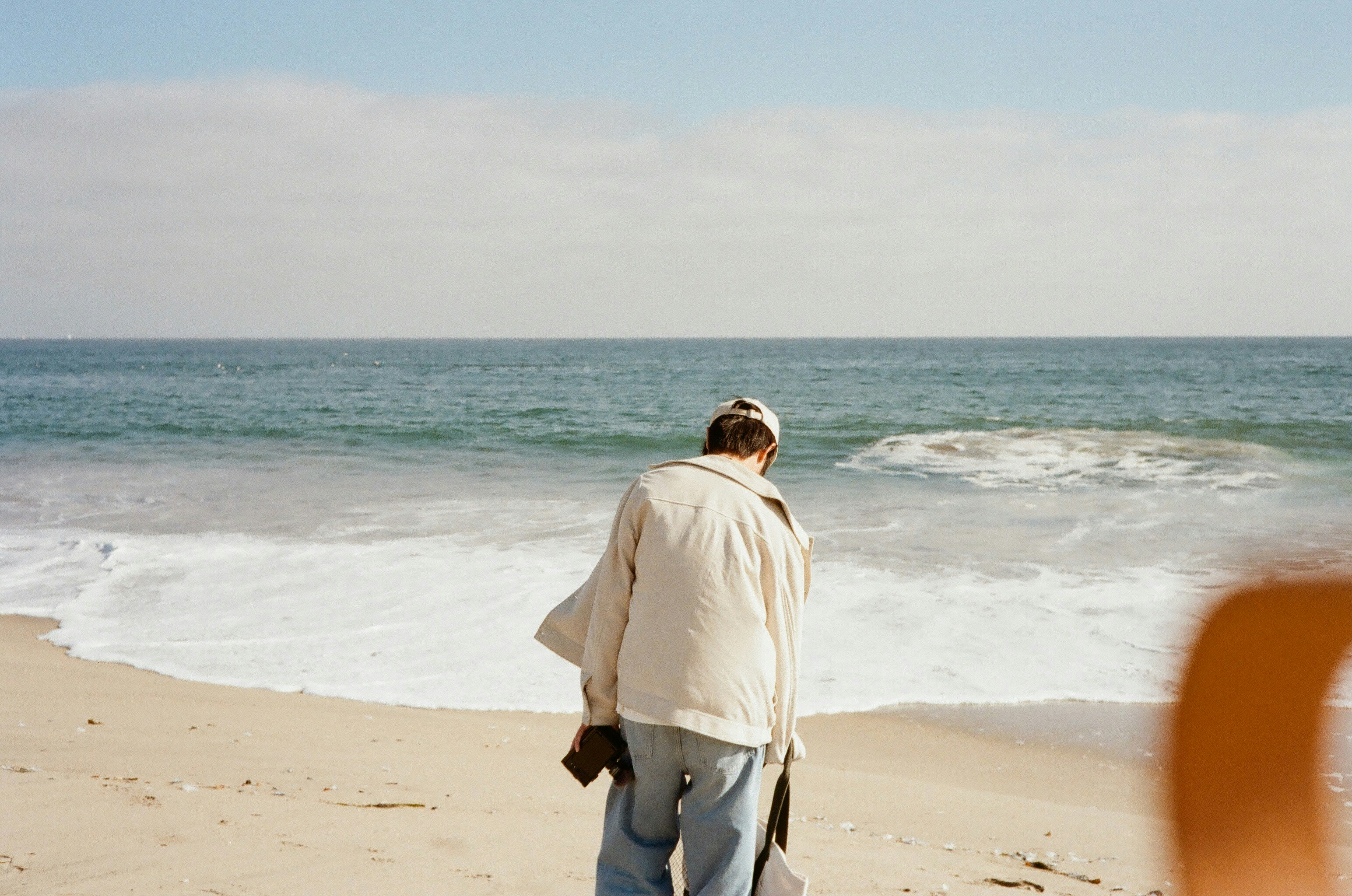 Back view of person standing on sandy beach by ocean.