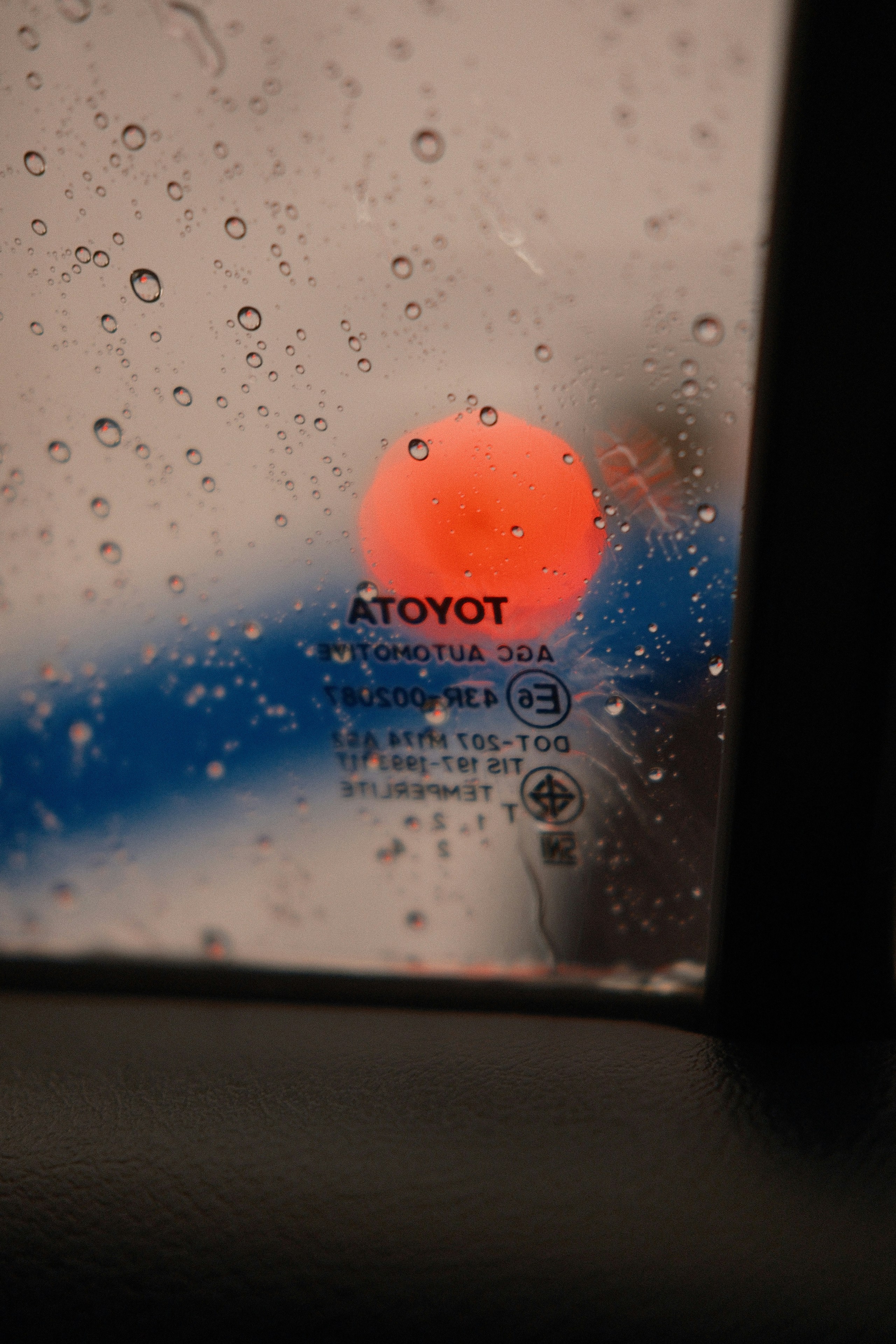 Rain-splashed window with a red sunset globe and reflected logo