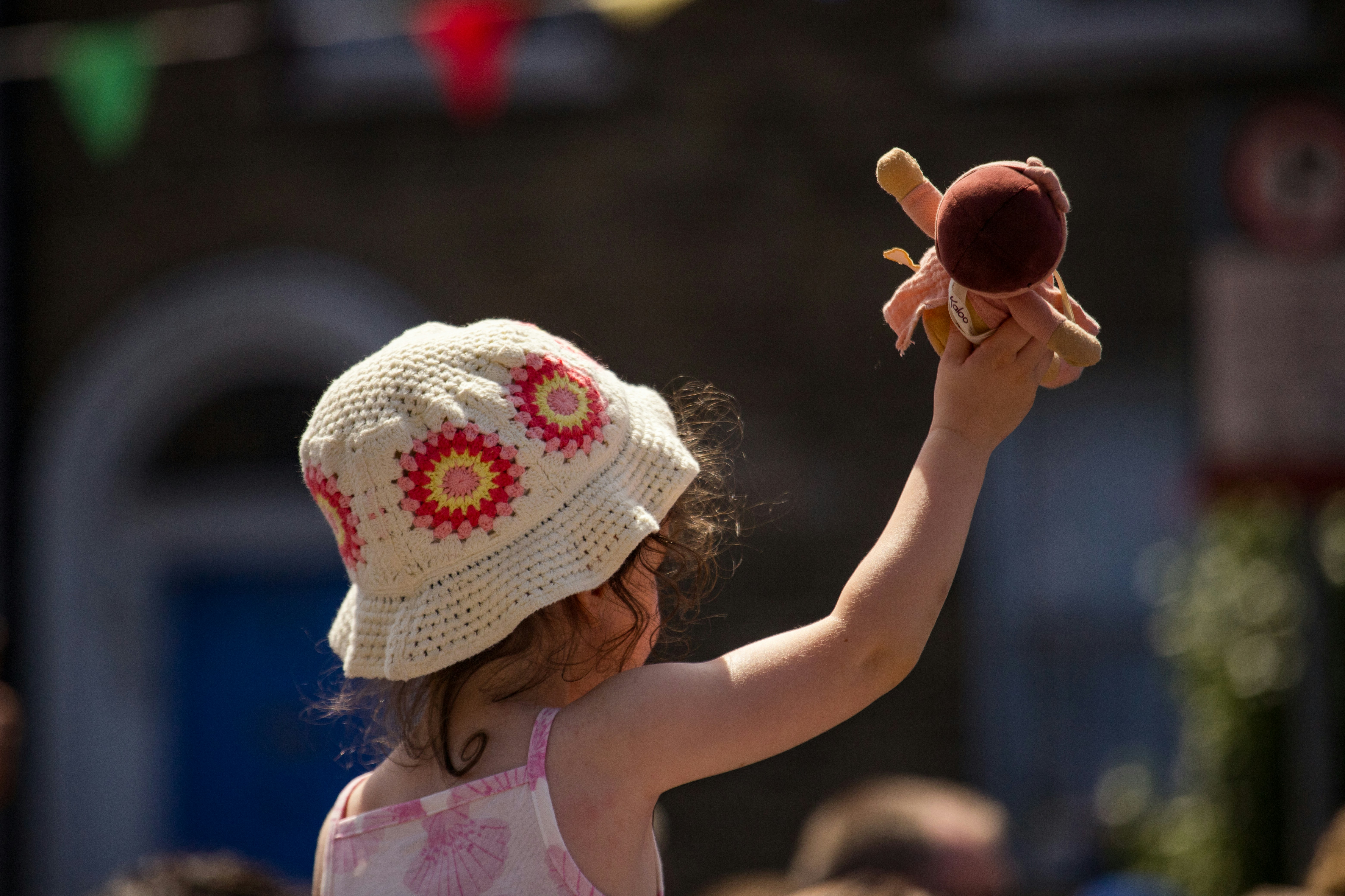 Child with raised stuffed toy and knit hat in sunlit outdoor scene