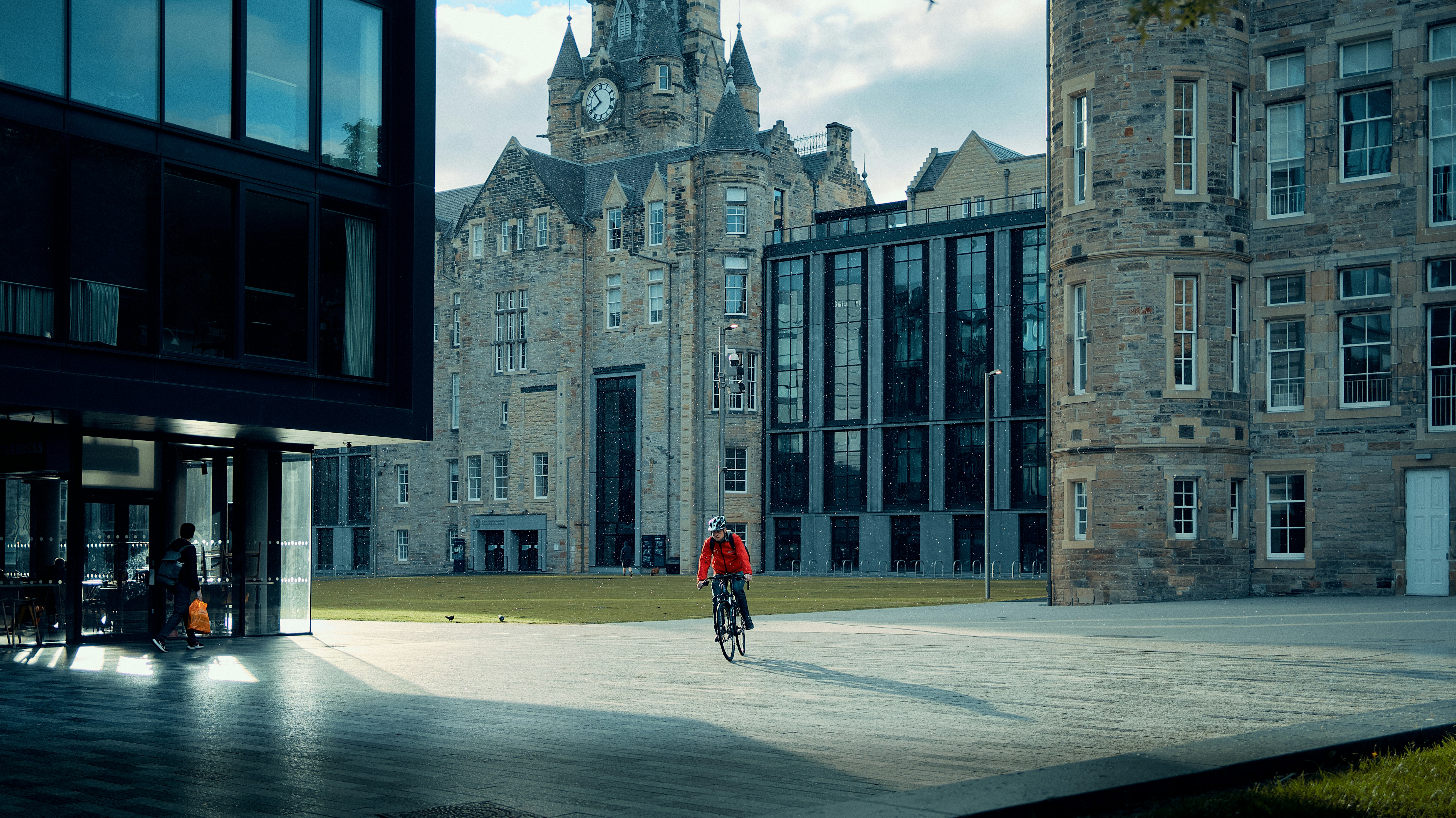 Red-clad Cyclist Crossing a Modern Courtyard Befriended by Historic Stone Architecture