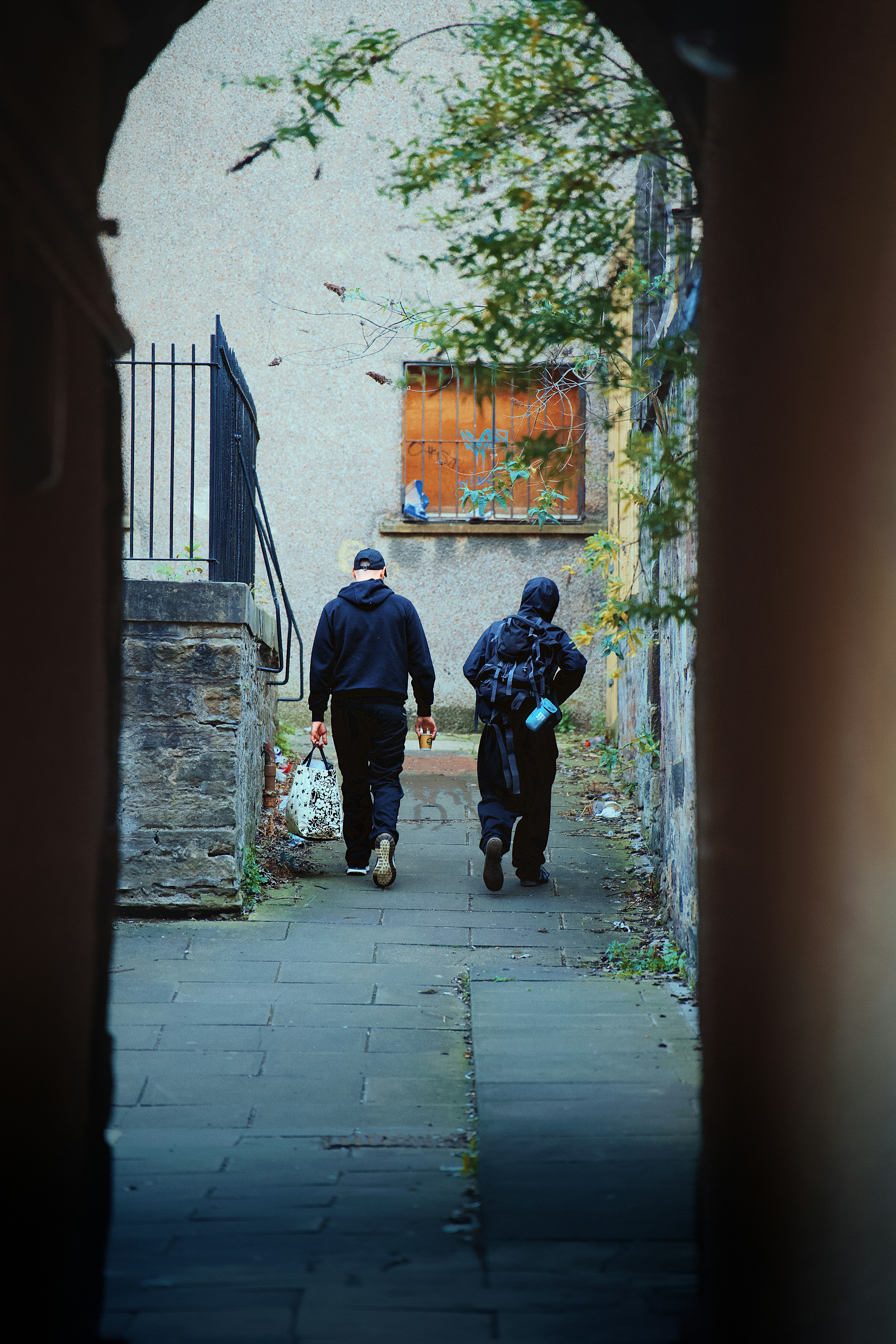 Two Travelers Walk Through a Narrow Courtyard Toward a Distant Gate
