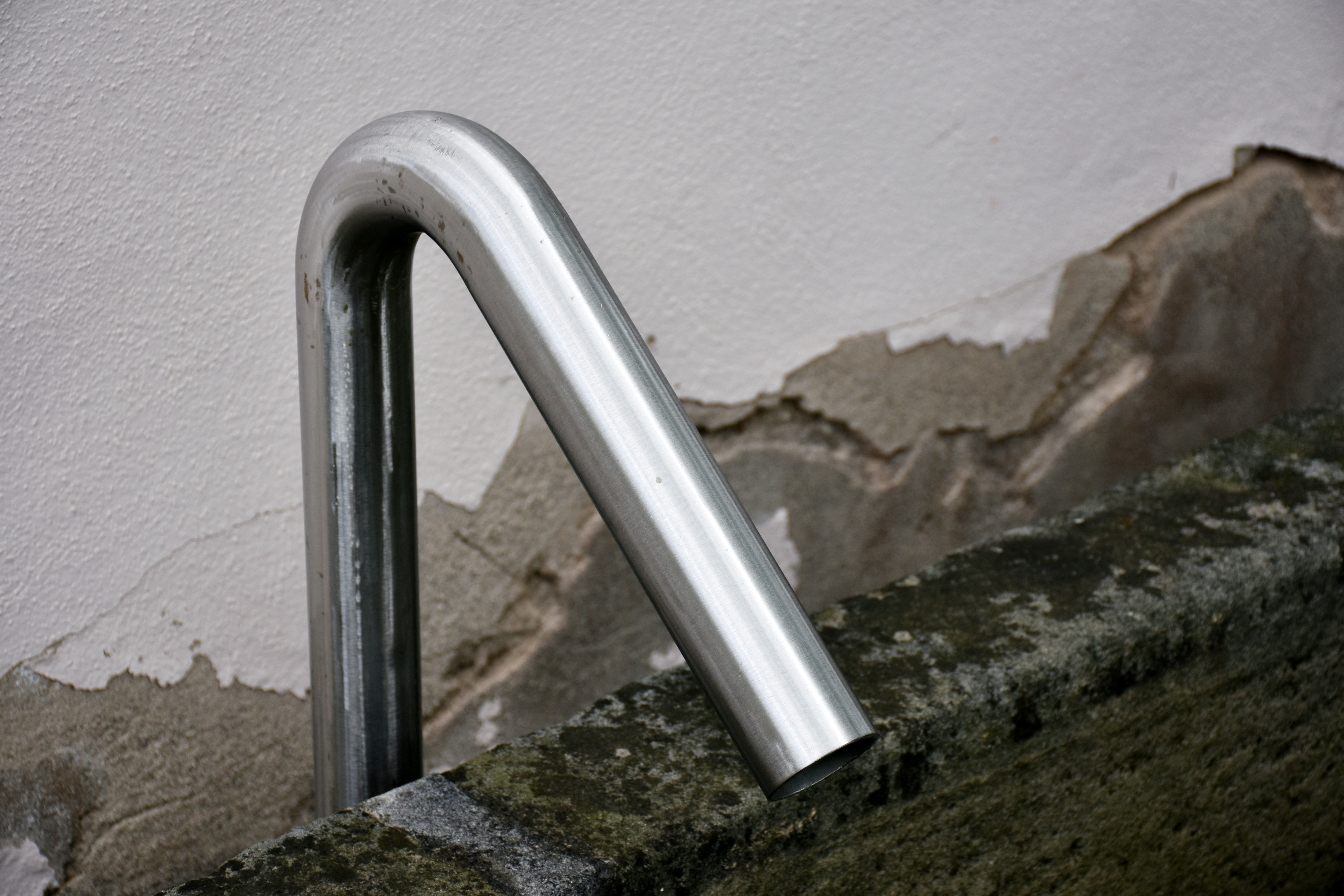 Curved stainless arc: a lone handrail emerging from rough concrete