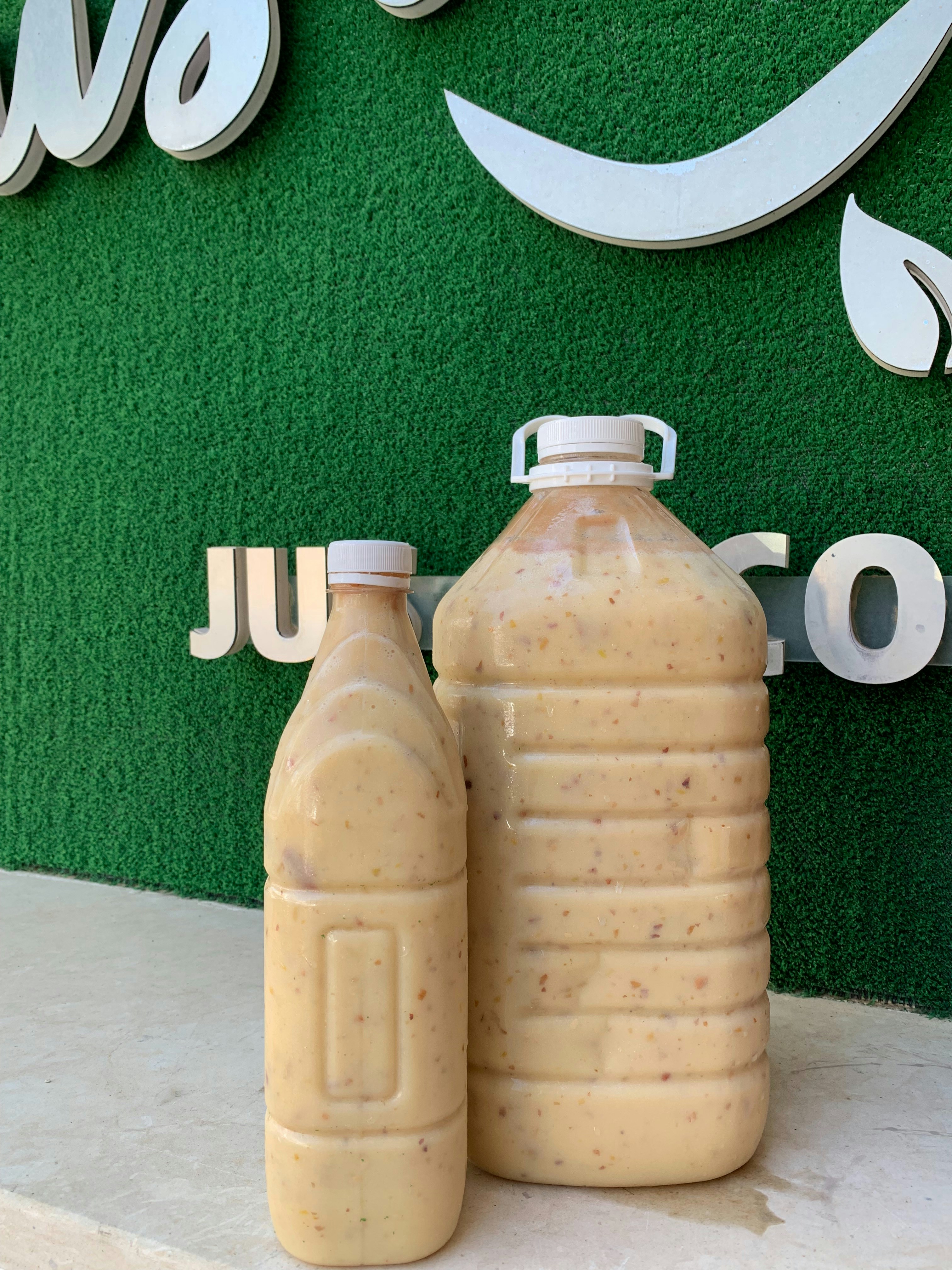 Two bereit bottles of smoothie on a concrete ledge in front of a green wall