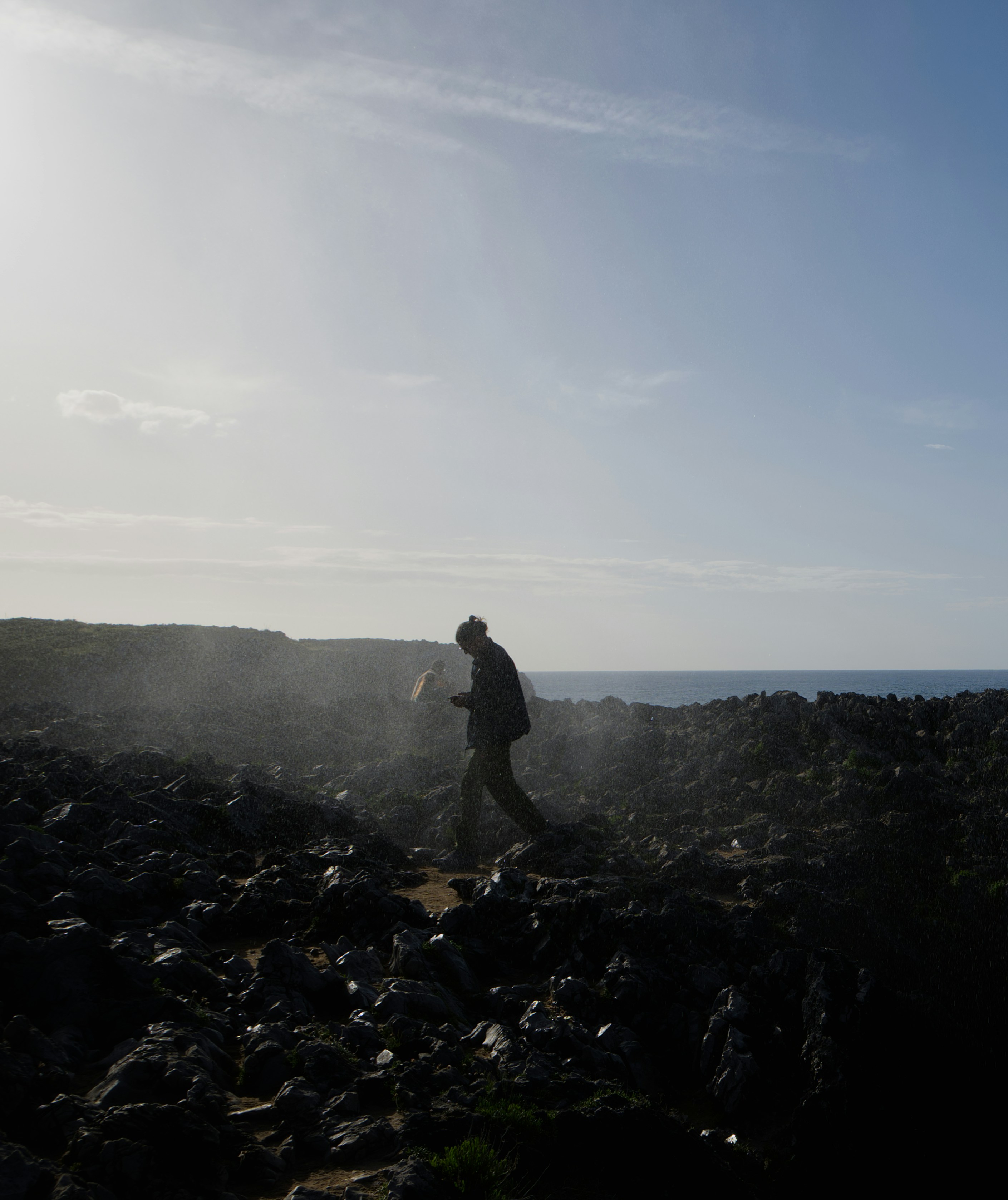 A lone wanderer traces a path across volcanic flats toward the sea