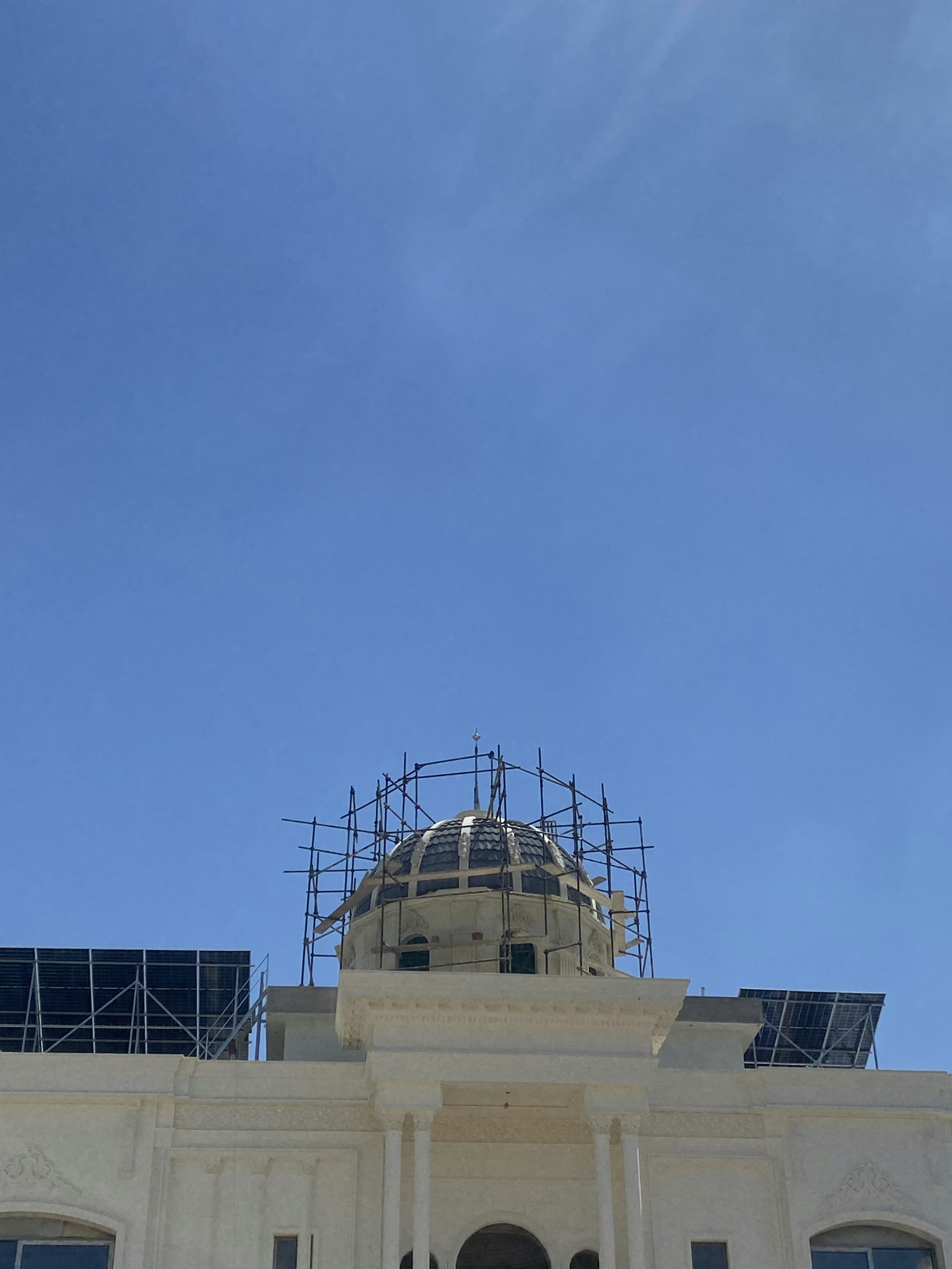 Clear blue sky over a white classical building with a domed structure surrounded by scaffolding, emphasizing architectural detail and vertical rise.