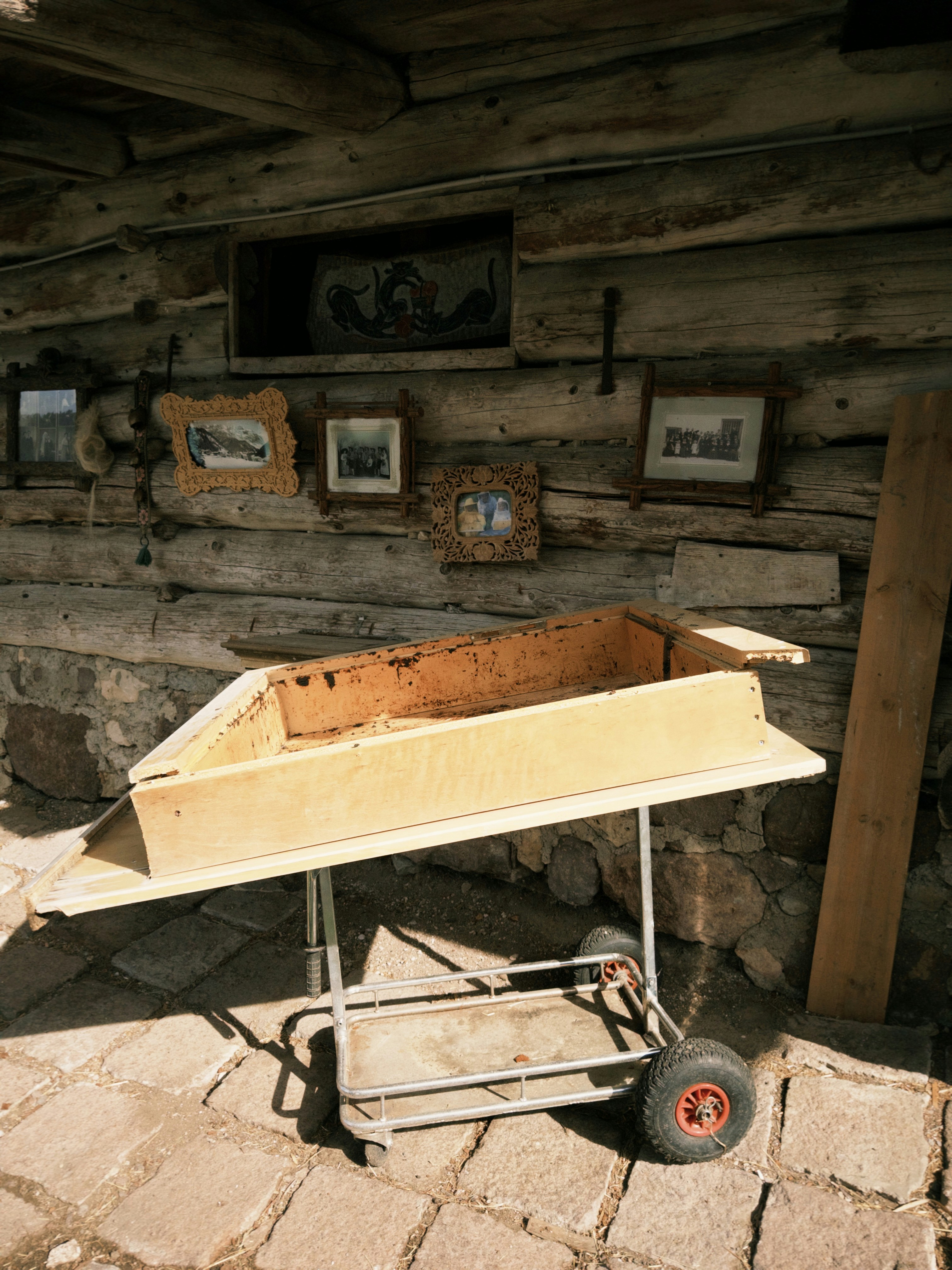 Sunlit wooden casket on a wheeled stand inside a rustic cabin