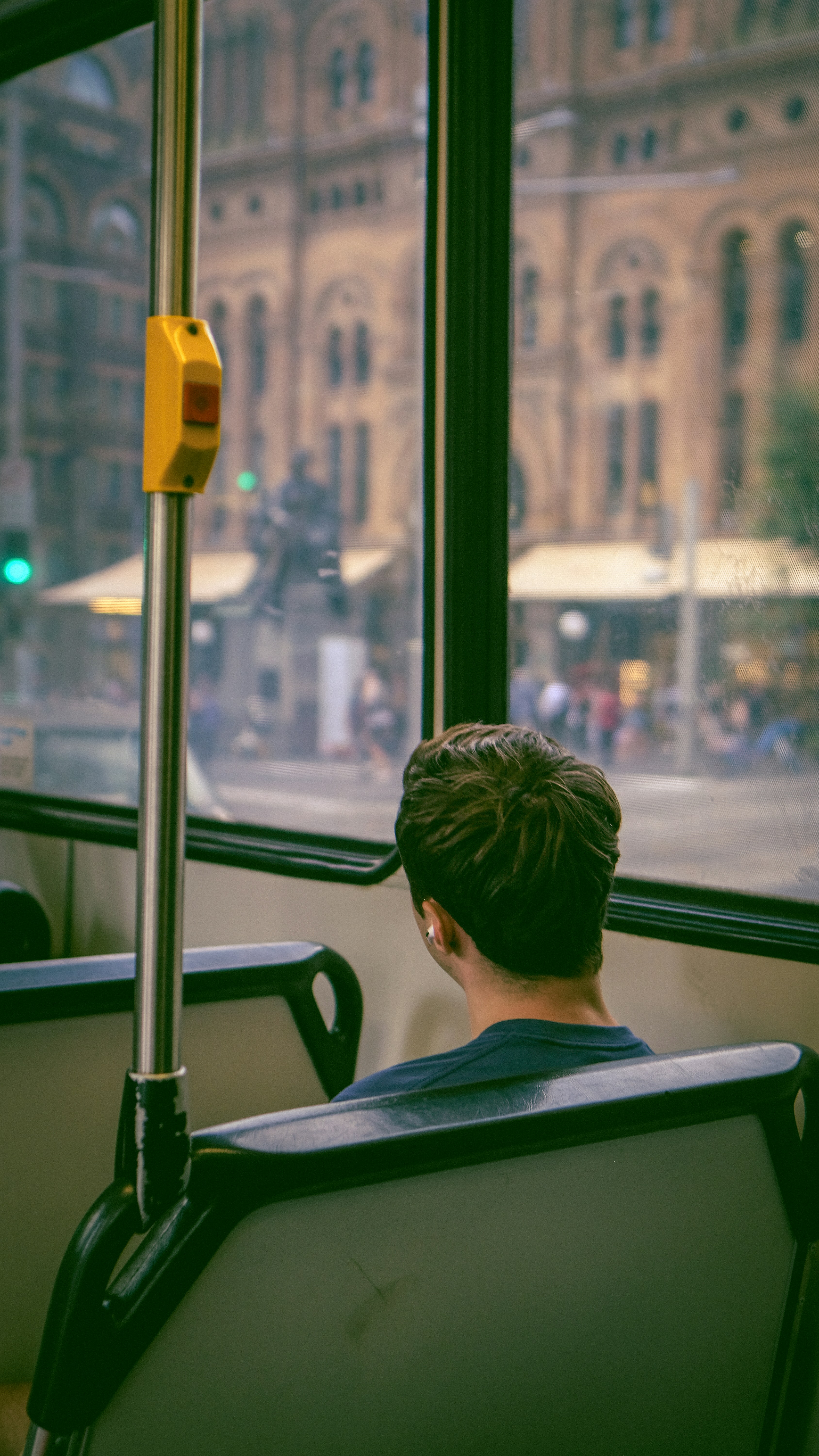 Backlit Bus Ride: A Passenger Faces the City’s Stone Facade