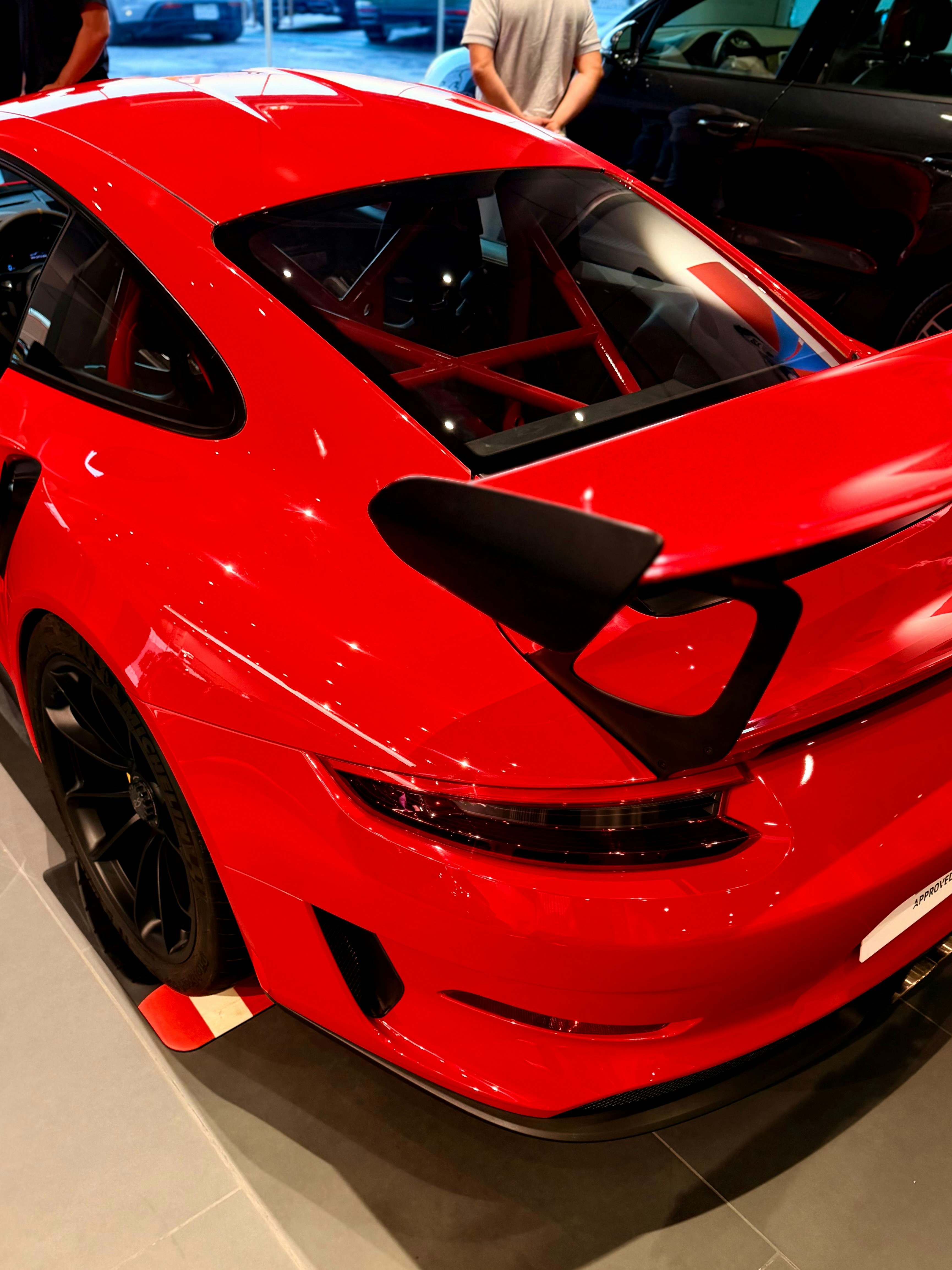 Glossy red sports car rear quarter panel with wing spoiler and taillight details visible in a showroom.