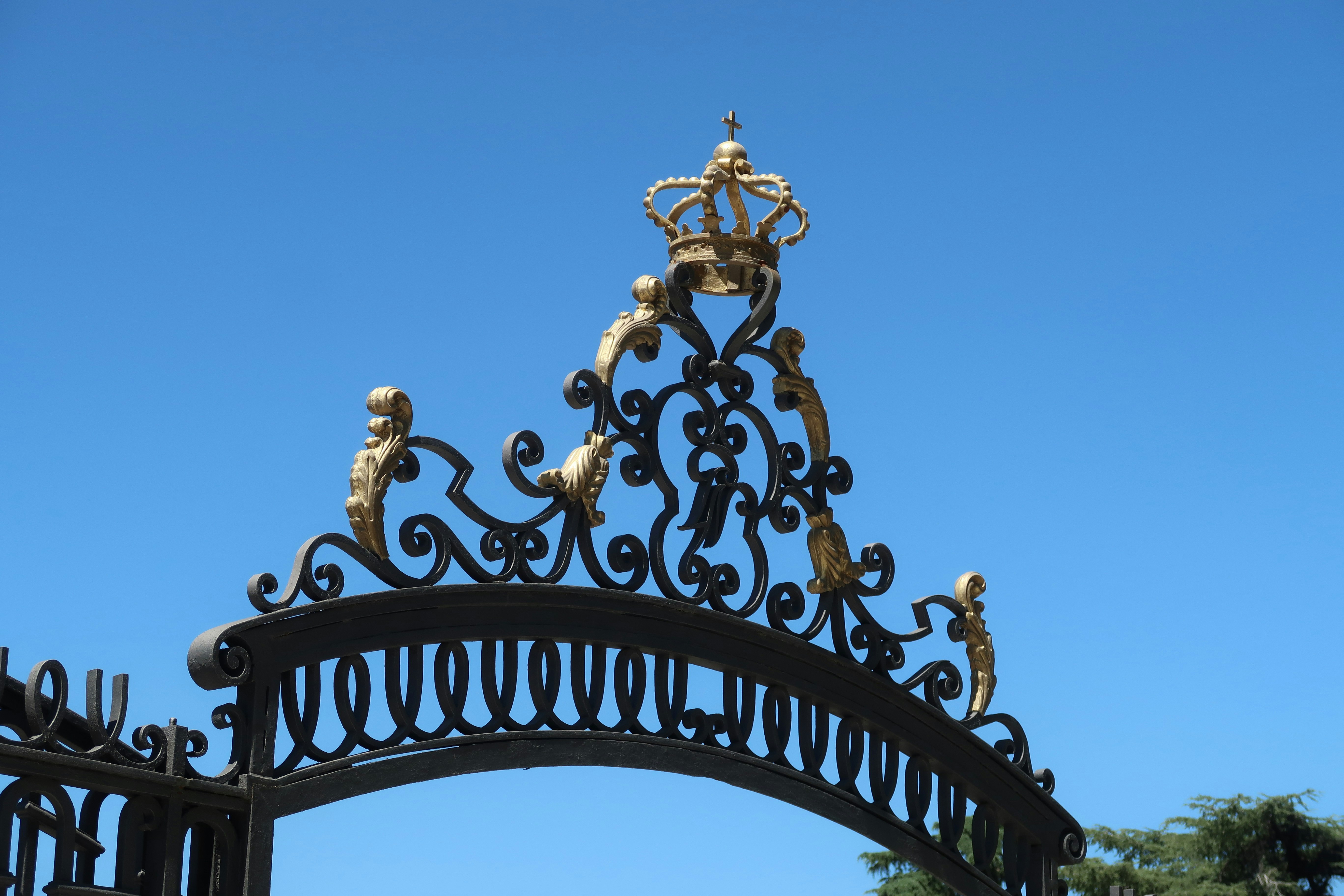 Ornate crown atop wrought-iron gateway against a clear blue sky